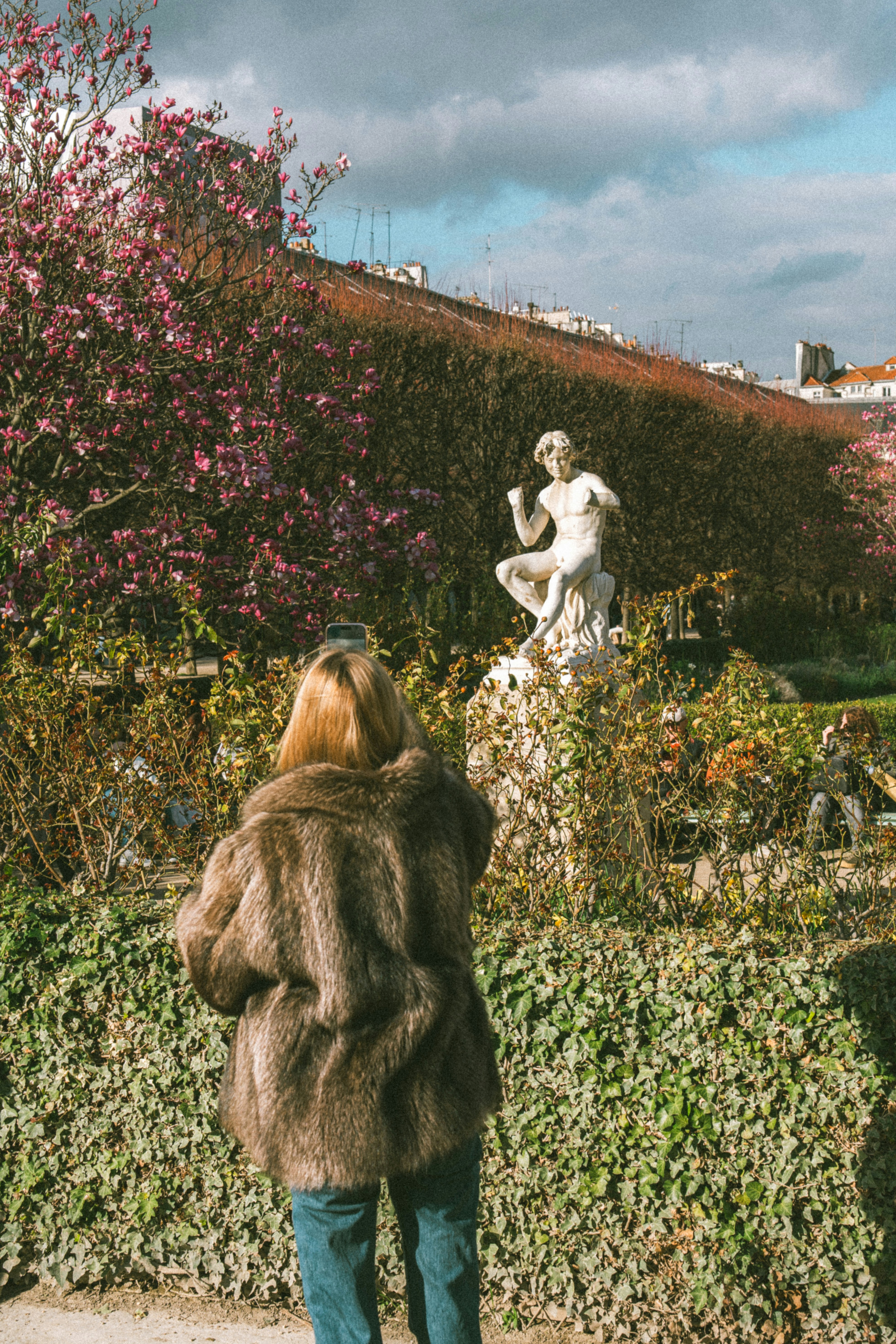 Fur-clad visitor captures a statue’s moment in a sunlit garden