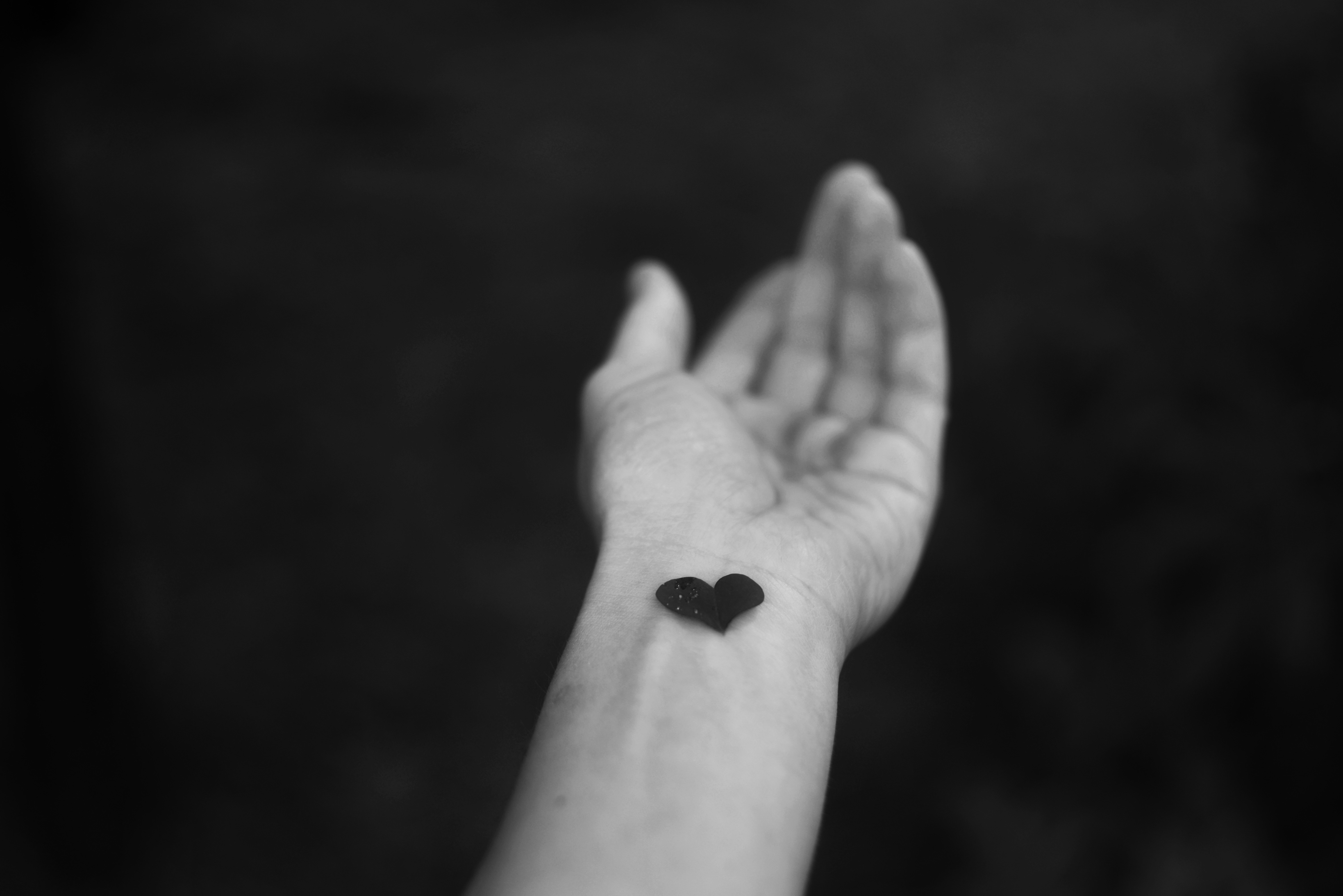 Raised palm reveals a tiny black heart: a minimalist tattoo of emotion