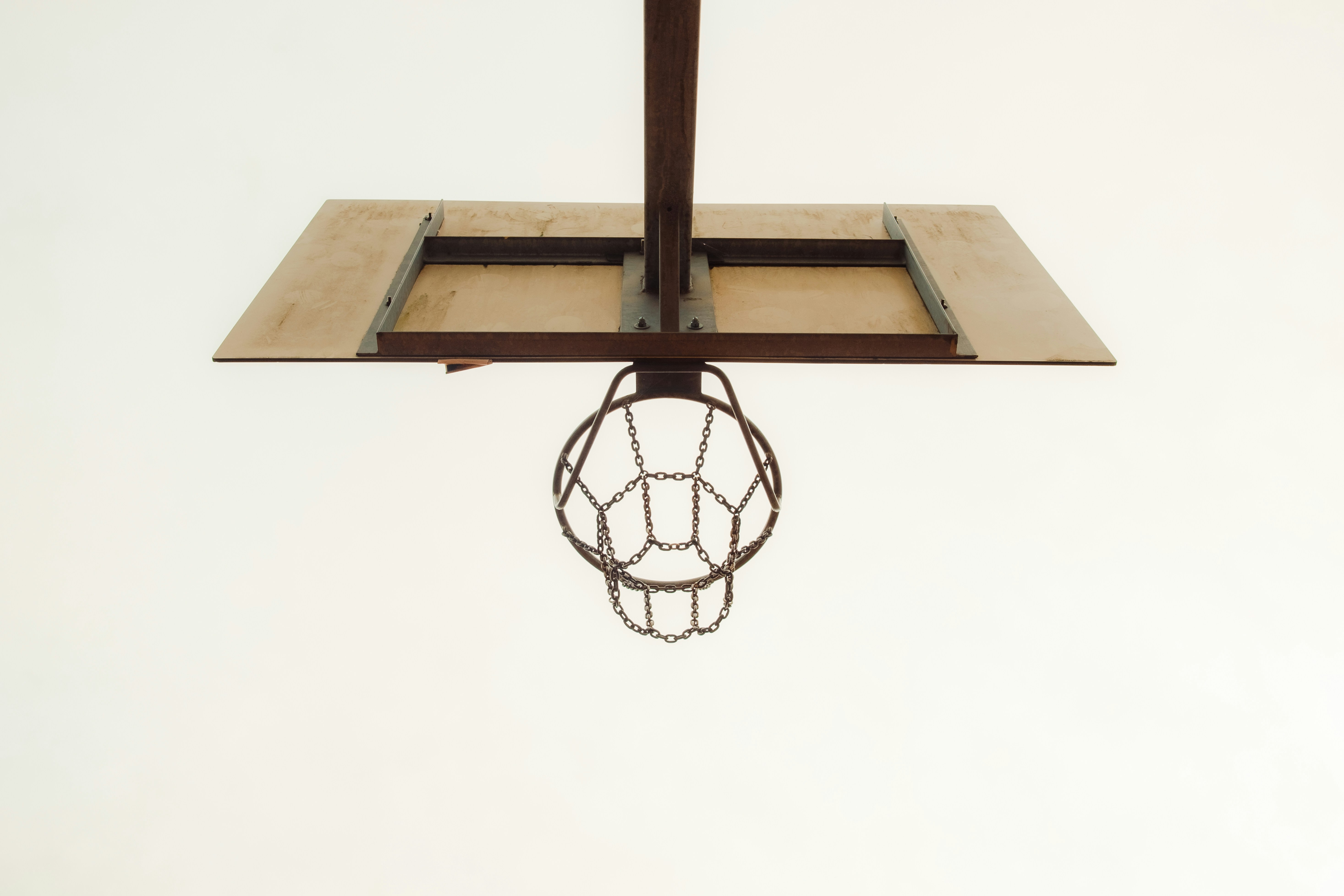 Symmetrical low angle shot of a metallic chain basketball hoop isolated against a bright sky.