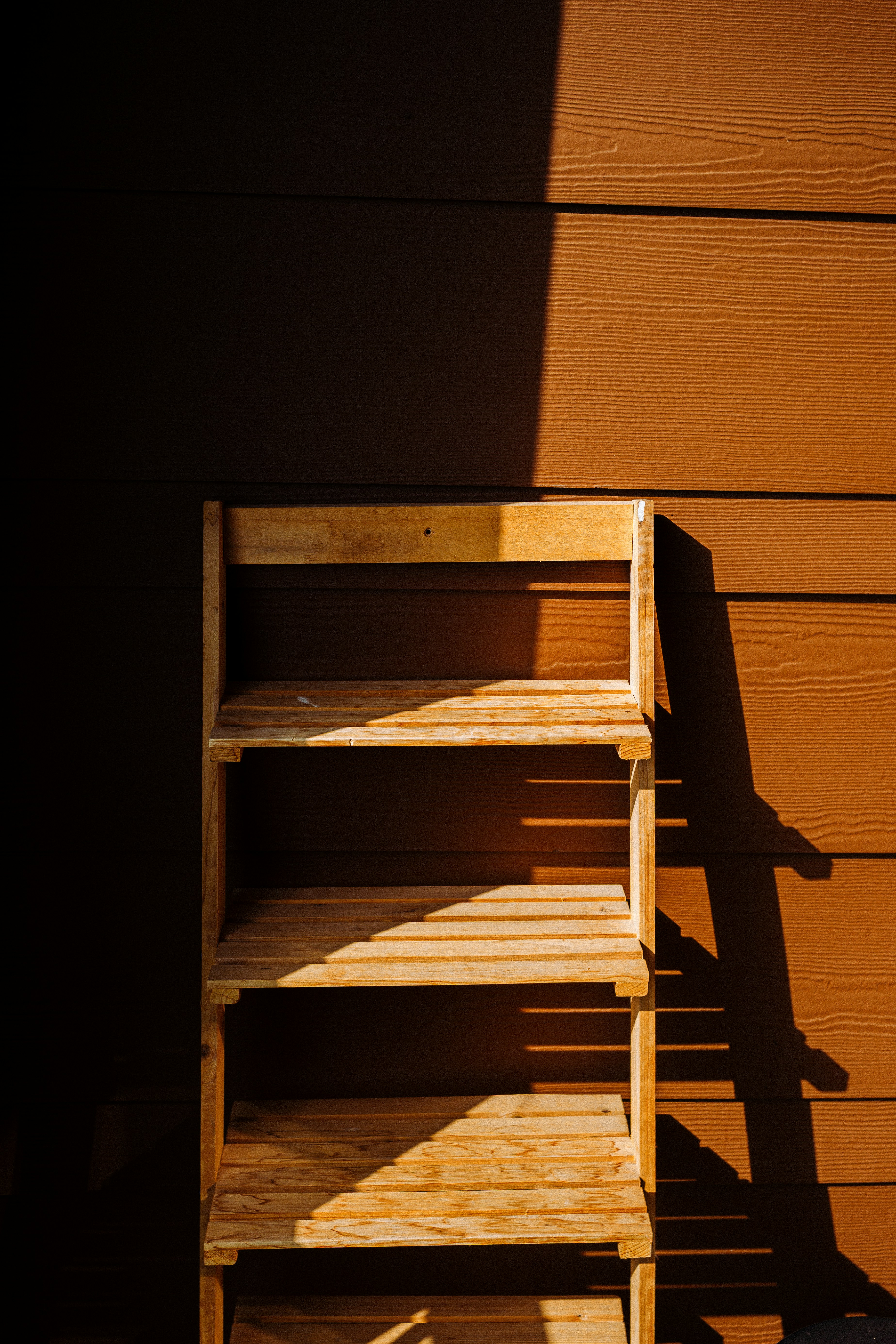 Sunlit Steps: A Wooden Shelf Cast in Shadow Against Orange Wall