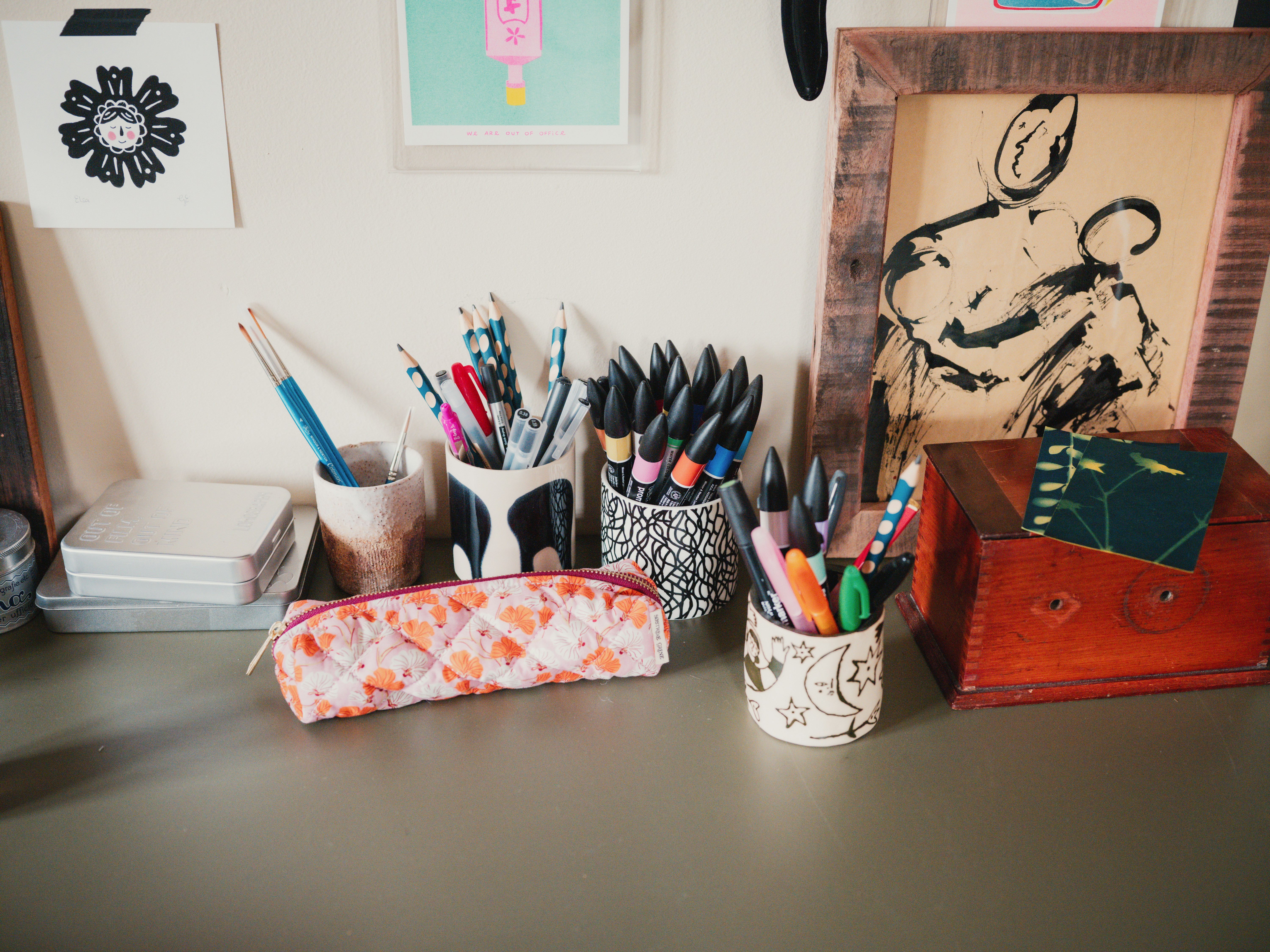 Workspace still life: pencil cups, art supplies and a framed figure on a sunlit desk