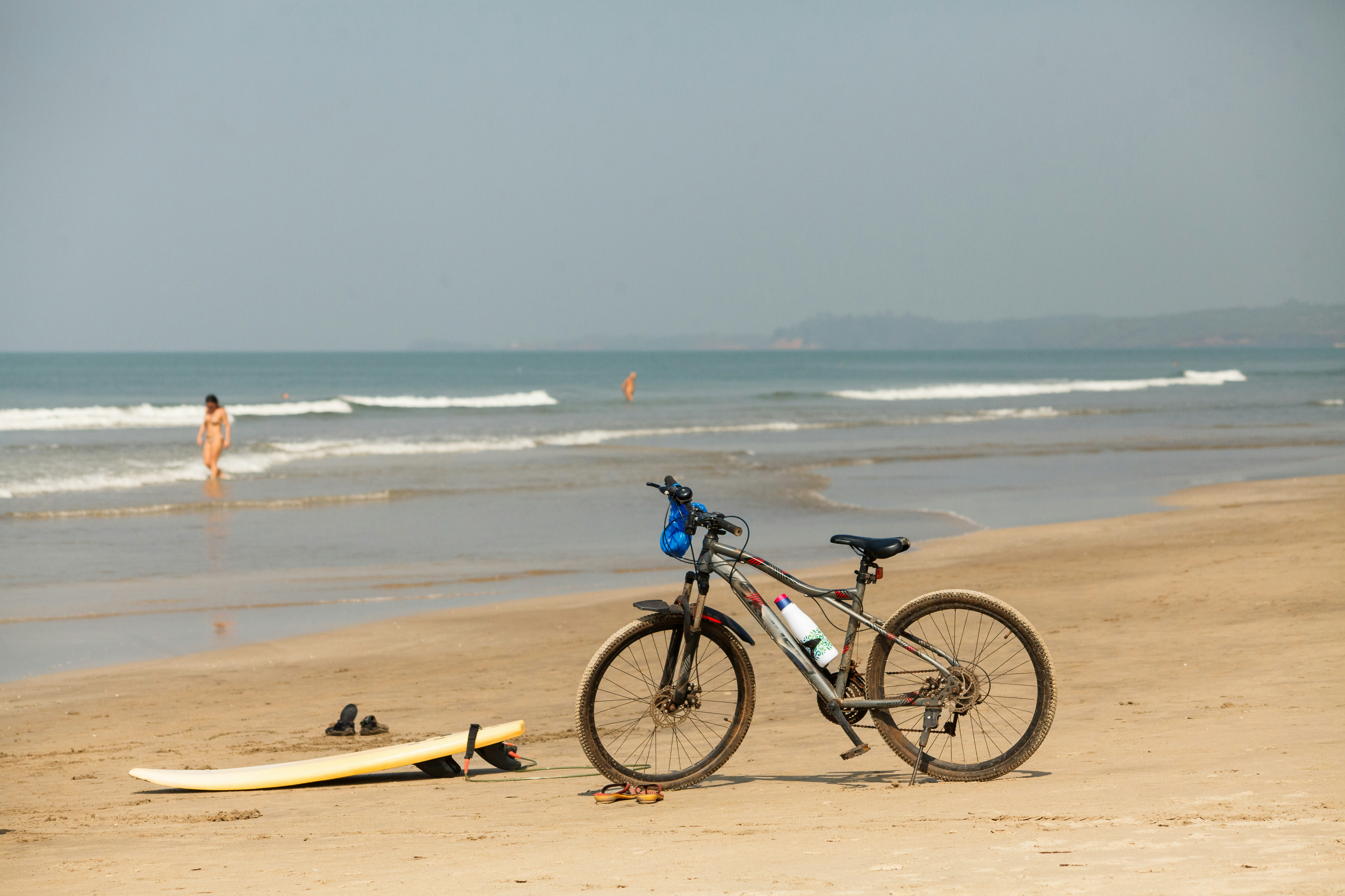 Sunlit Coastline: A Bike Resting on Wet Sand with Gentle Waves