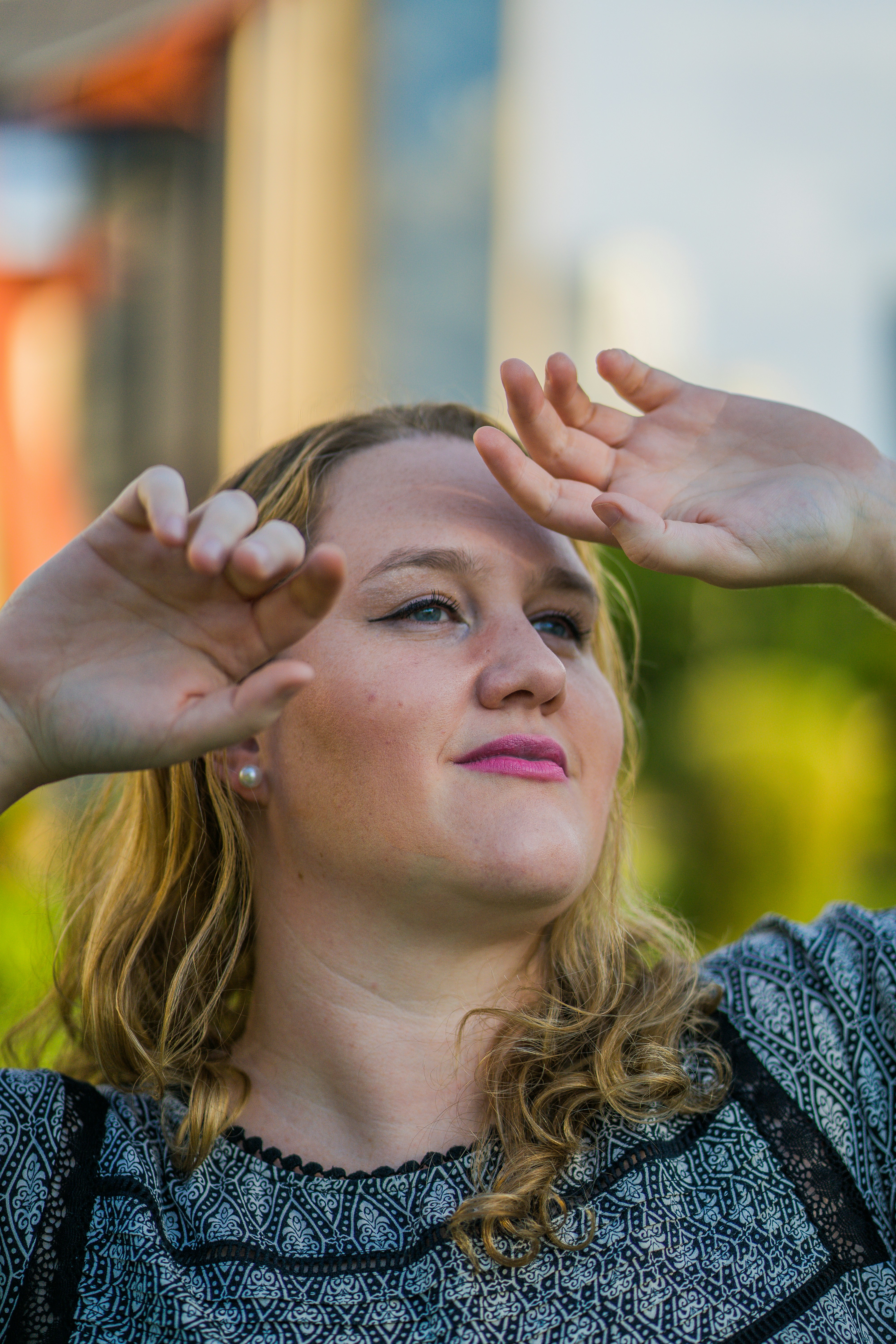 Sunlit Resolve: a portrait with hands raised against a blurred urban backdrop