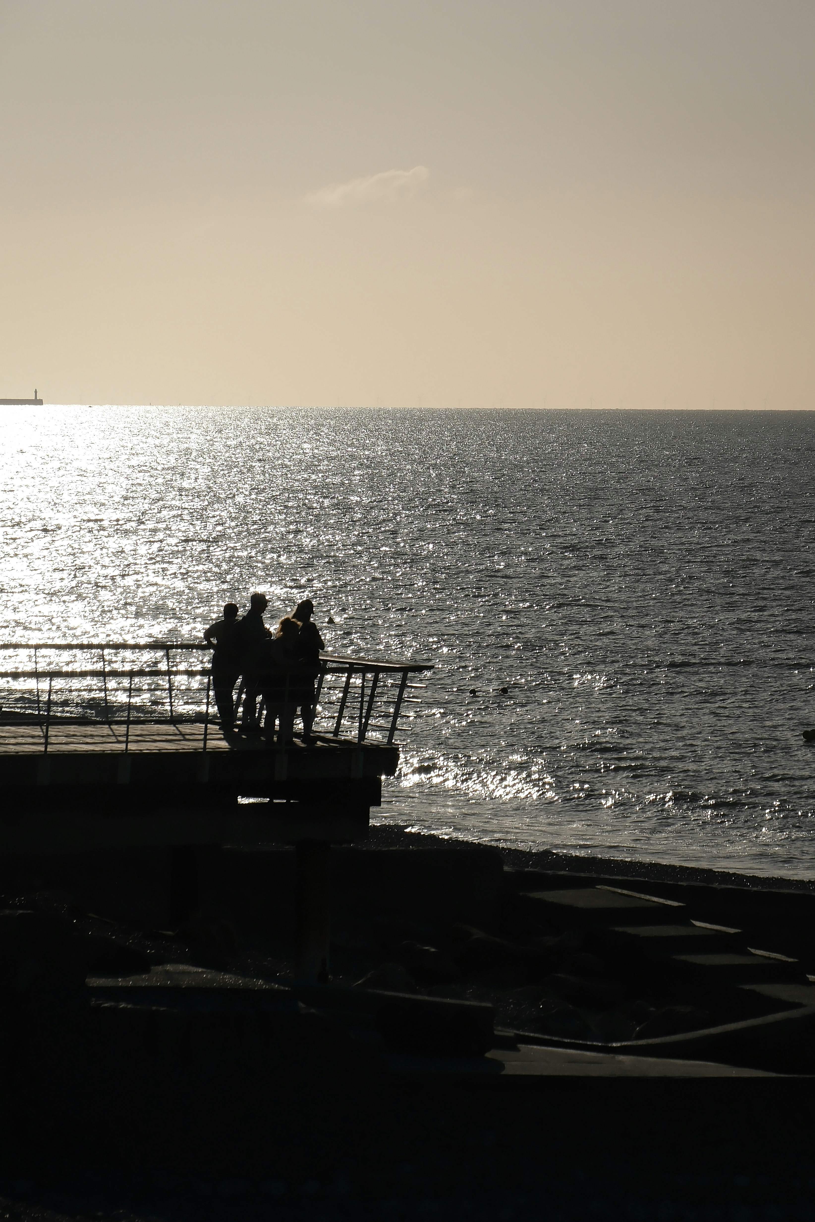  silhouettes on a sunlit pier at sea