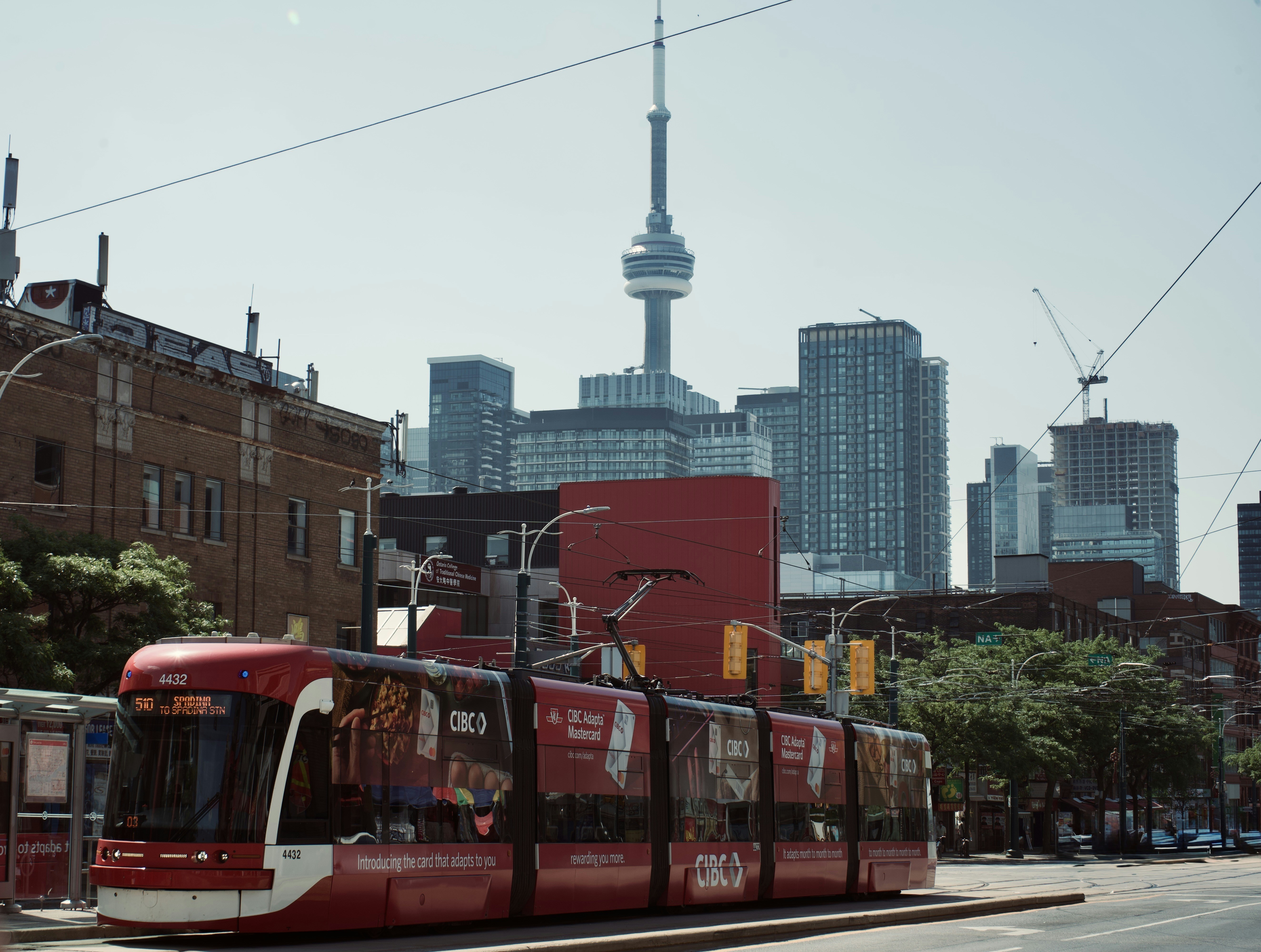 A red streetcar on tracks with the CN Tower in the Toronto skyline
