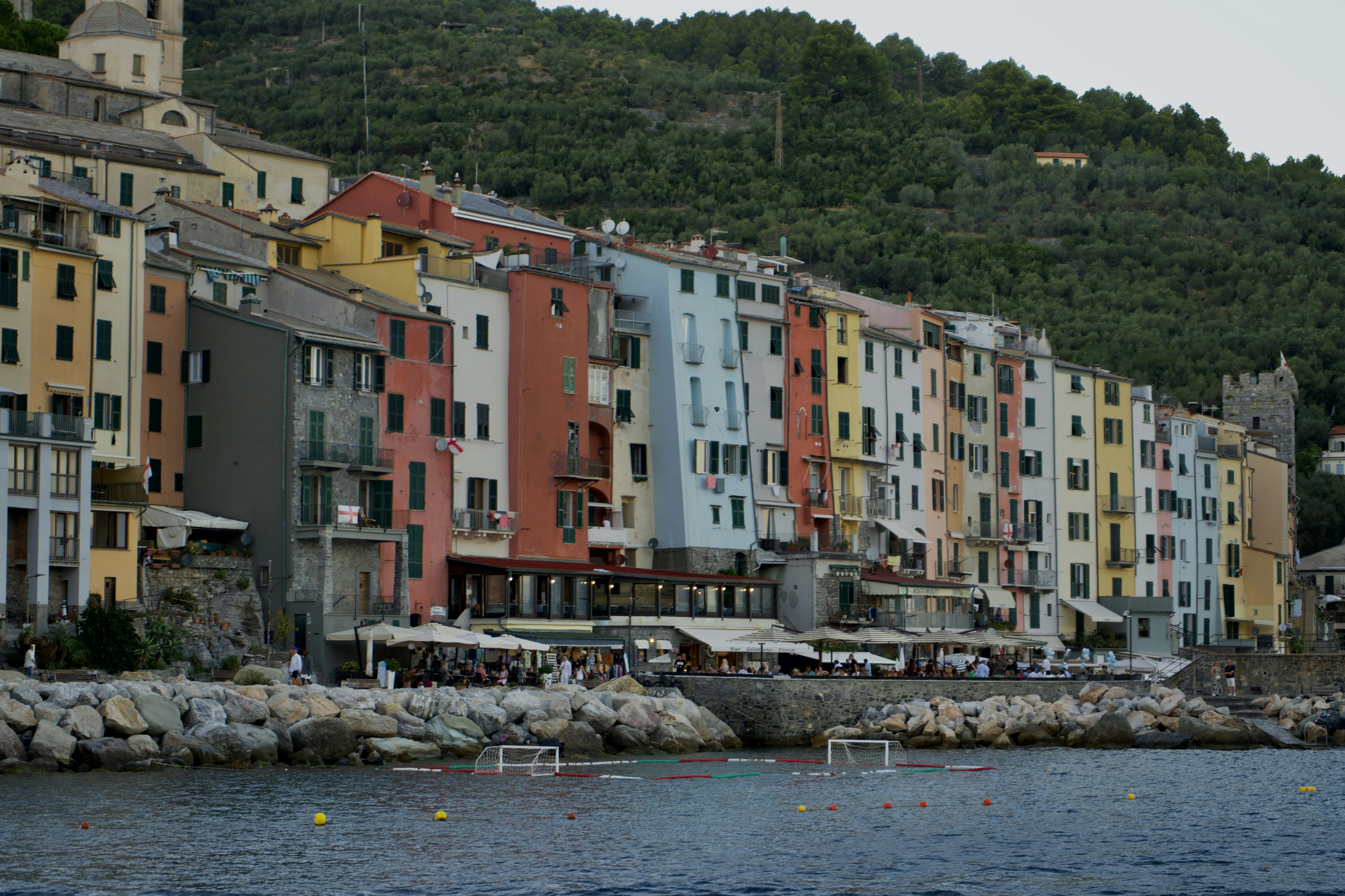 Colorful waterfront houses line the rocky quay under a green hillside