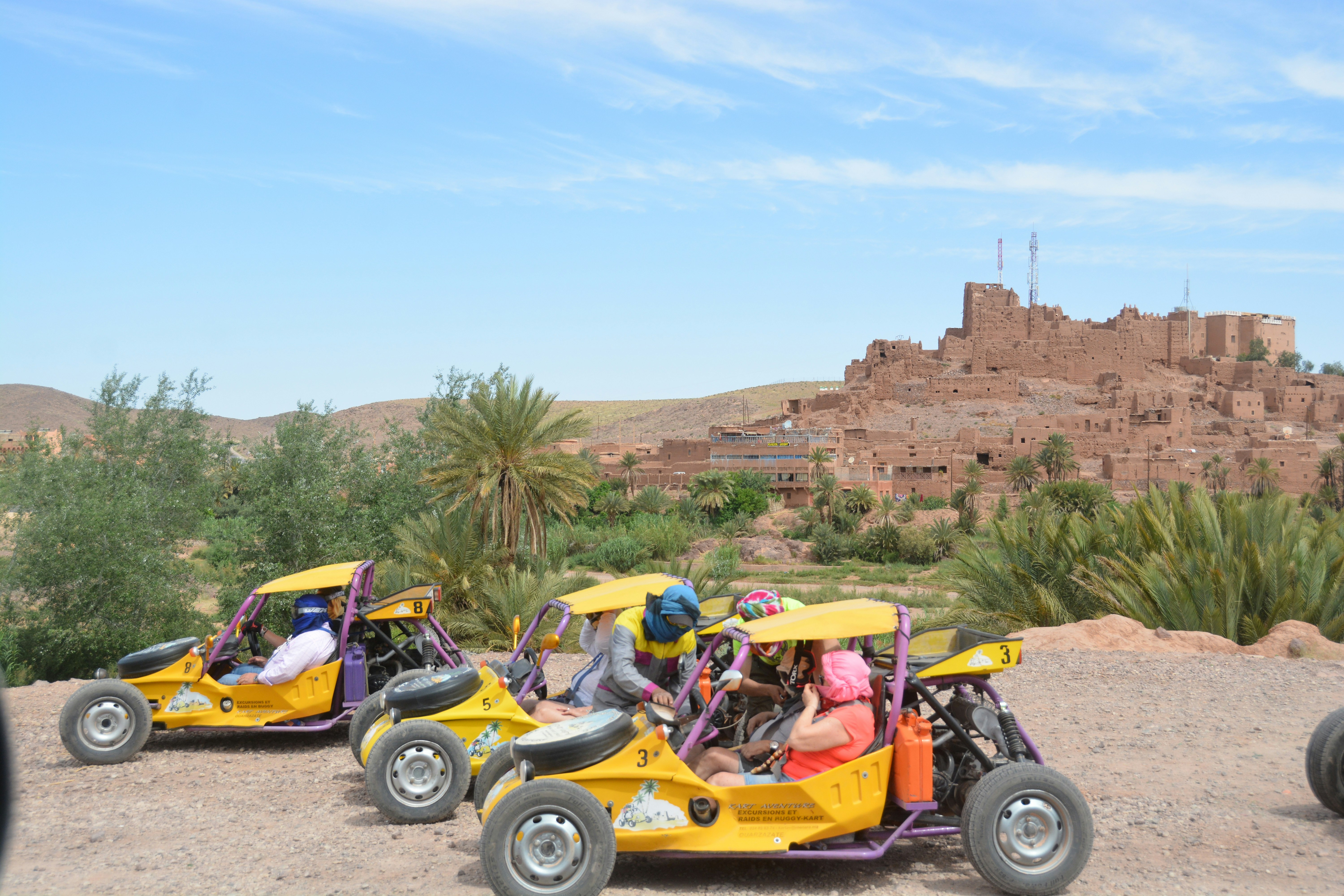 Yellow dune buggies line up toward a desert fortress under a bright blue sky