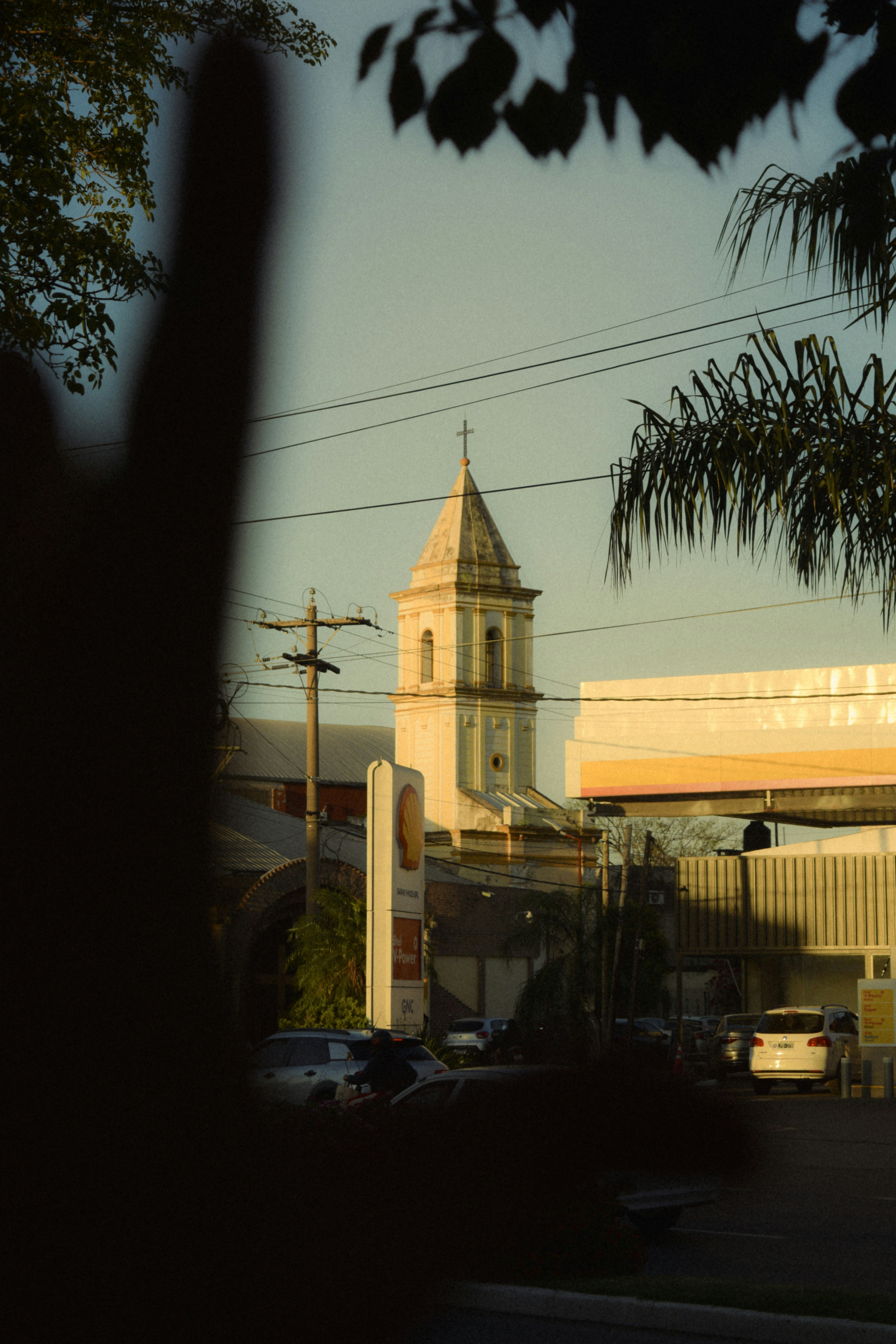 A church tower rising above a gas station at golden hour