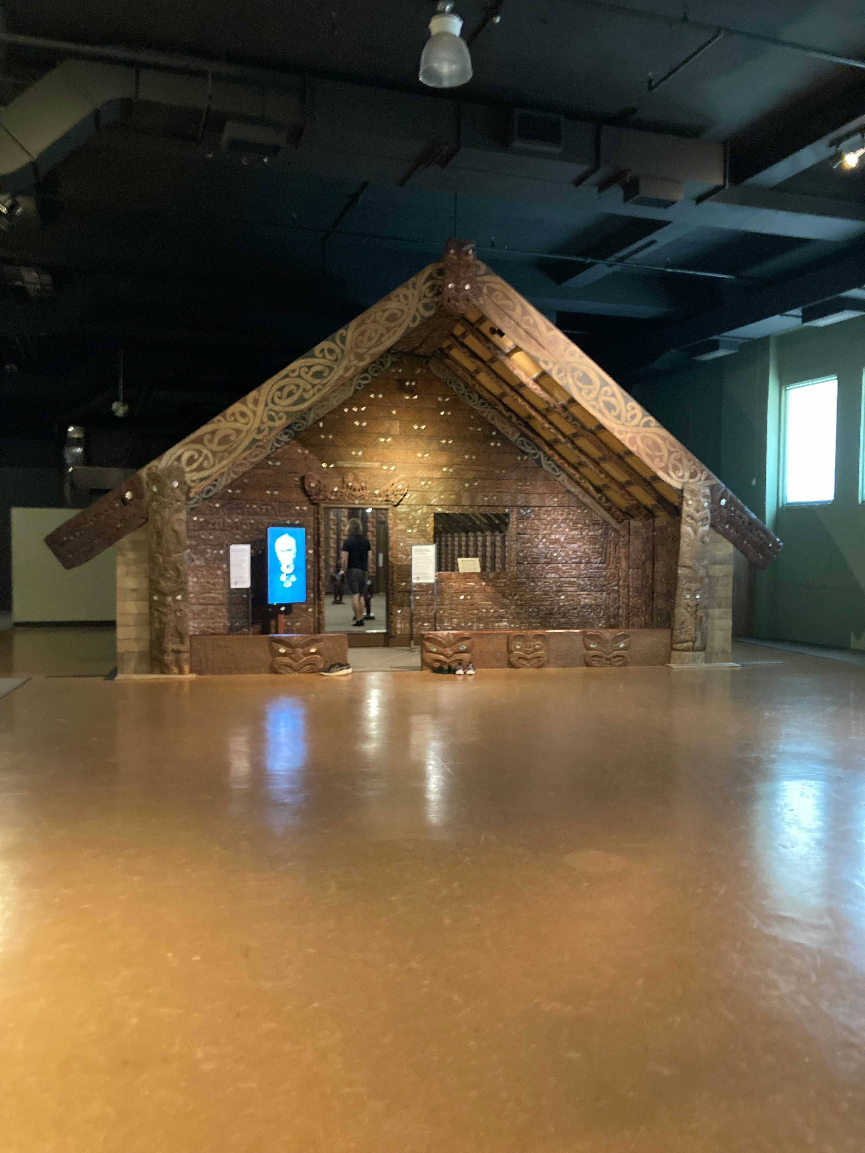Traditional wooden house exhibit anchored by a digital display