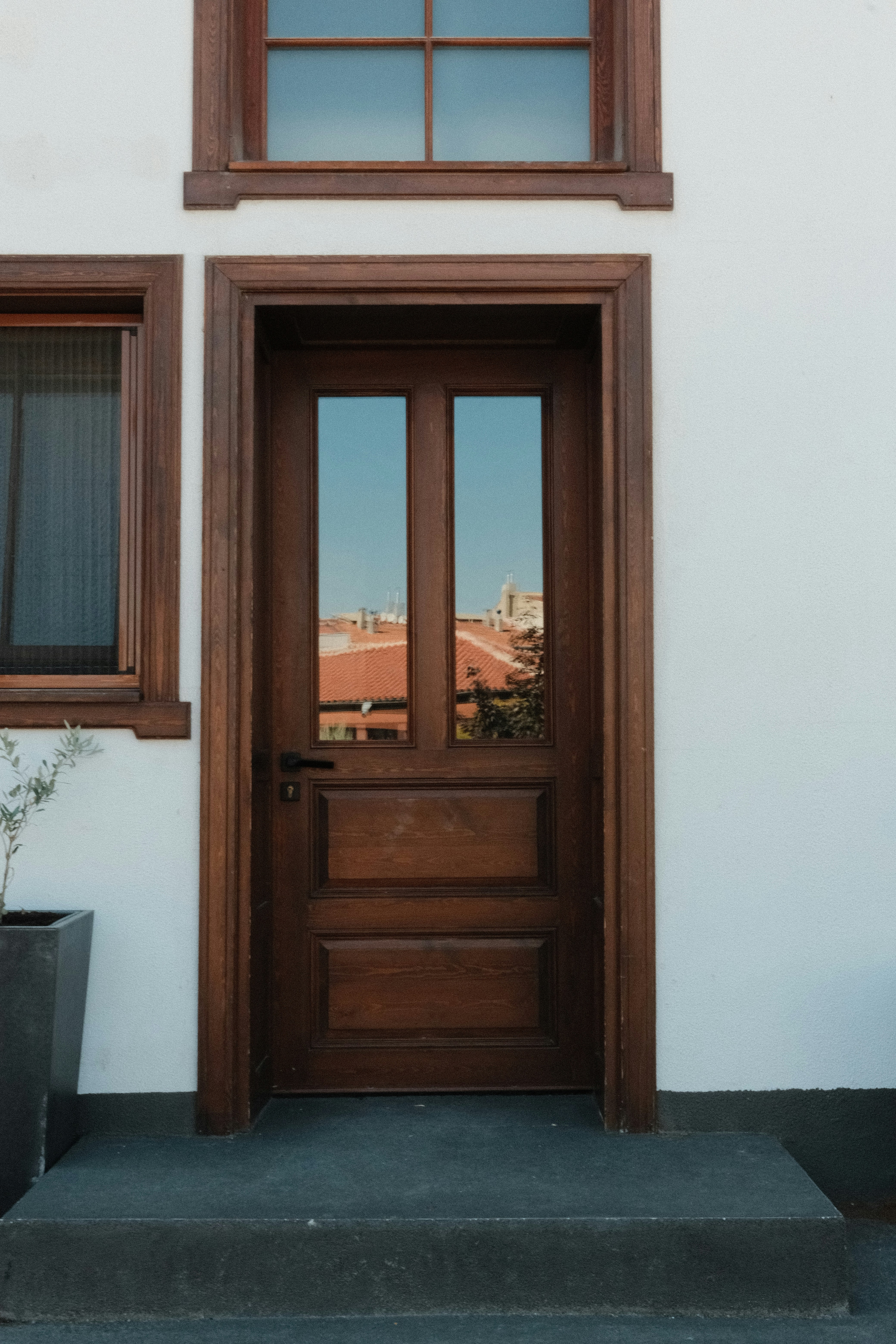 Wooden Door Framed by White Facade with Reflected Rooftops
