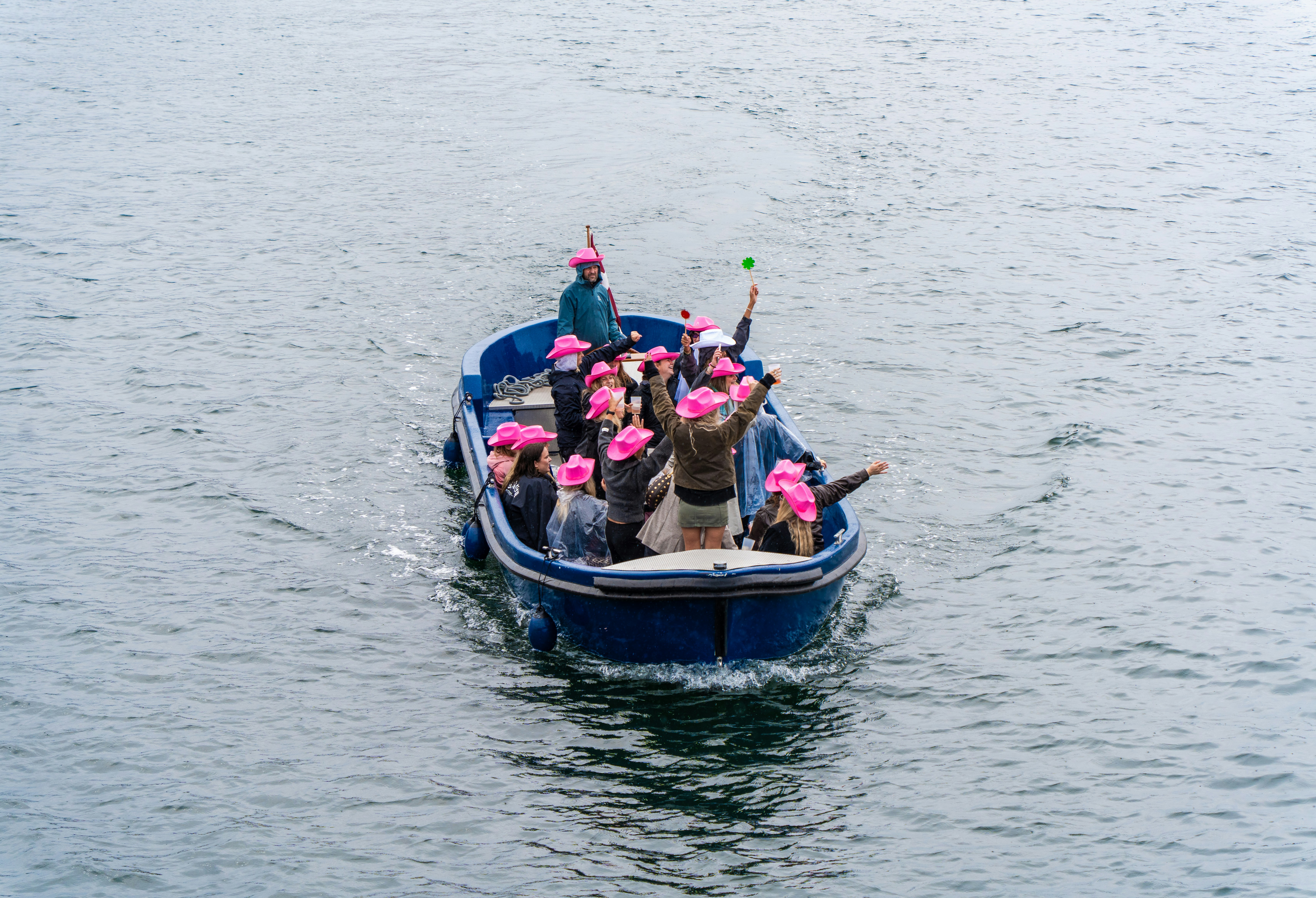 Joyful Parade: Passengers in Pink Hats Steer a Small Blue Boat Through Calm Waters