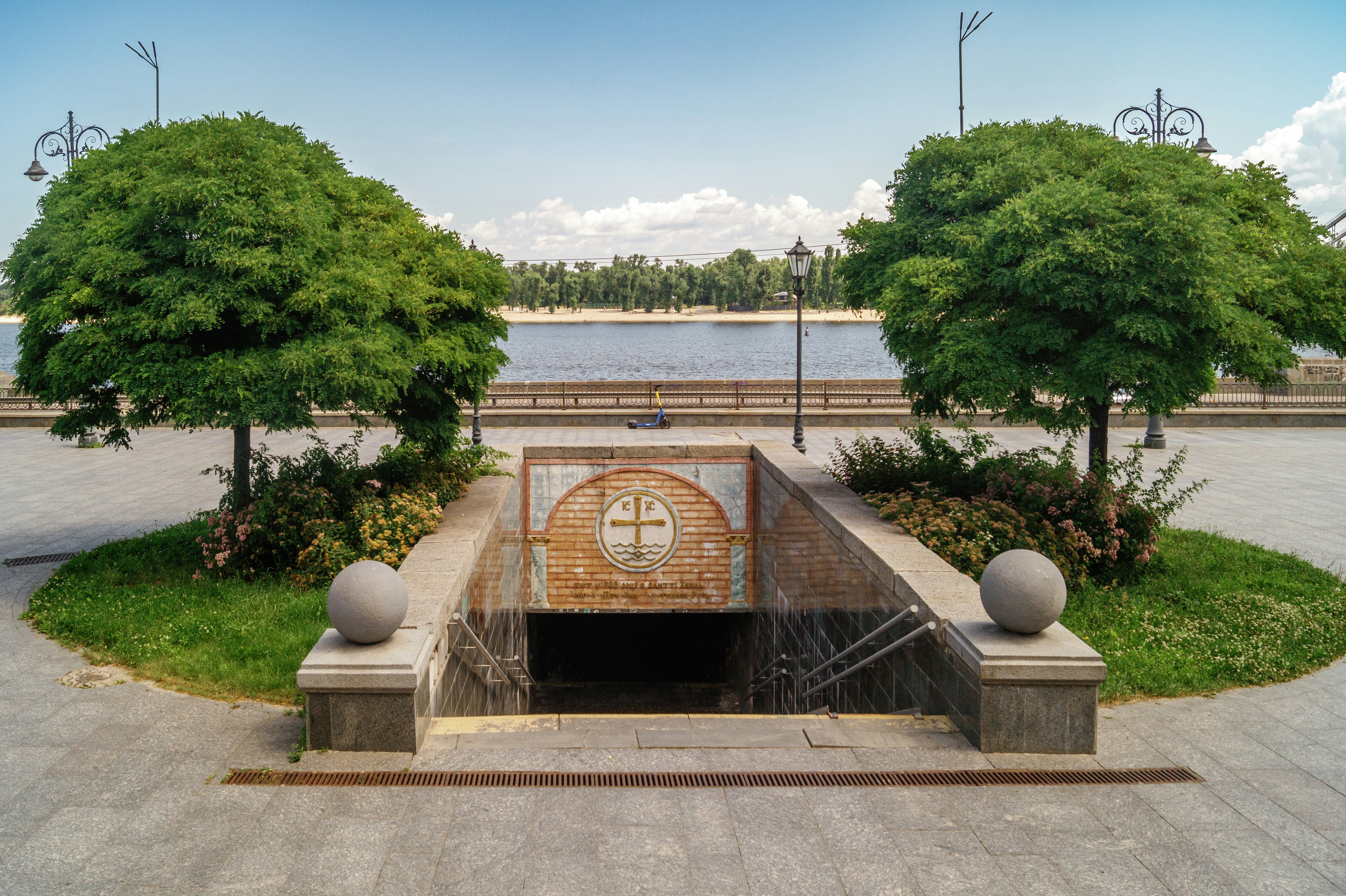 An underground pedestrian entrance with a religious mosaic near a river and trees