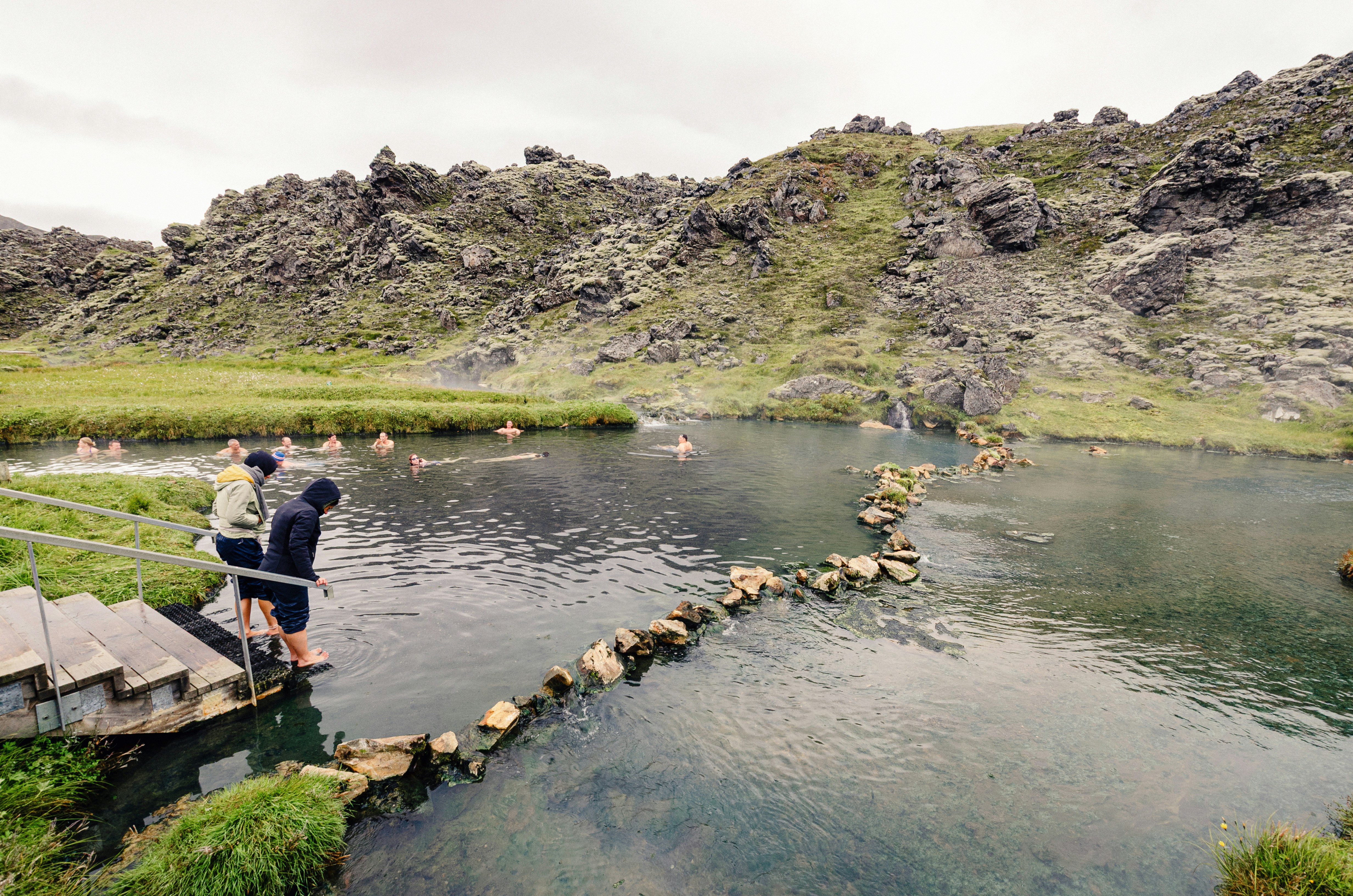 Steam and Stone: People Soak Above a Mummering Geothermal Pool