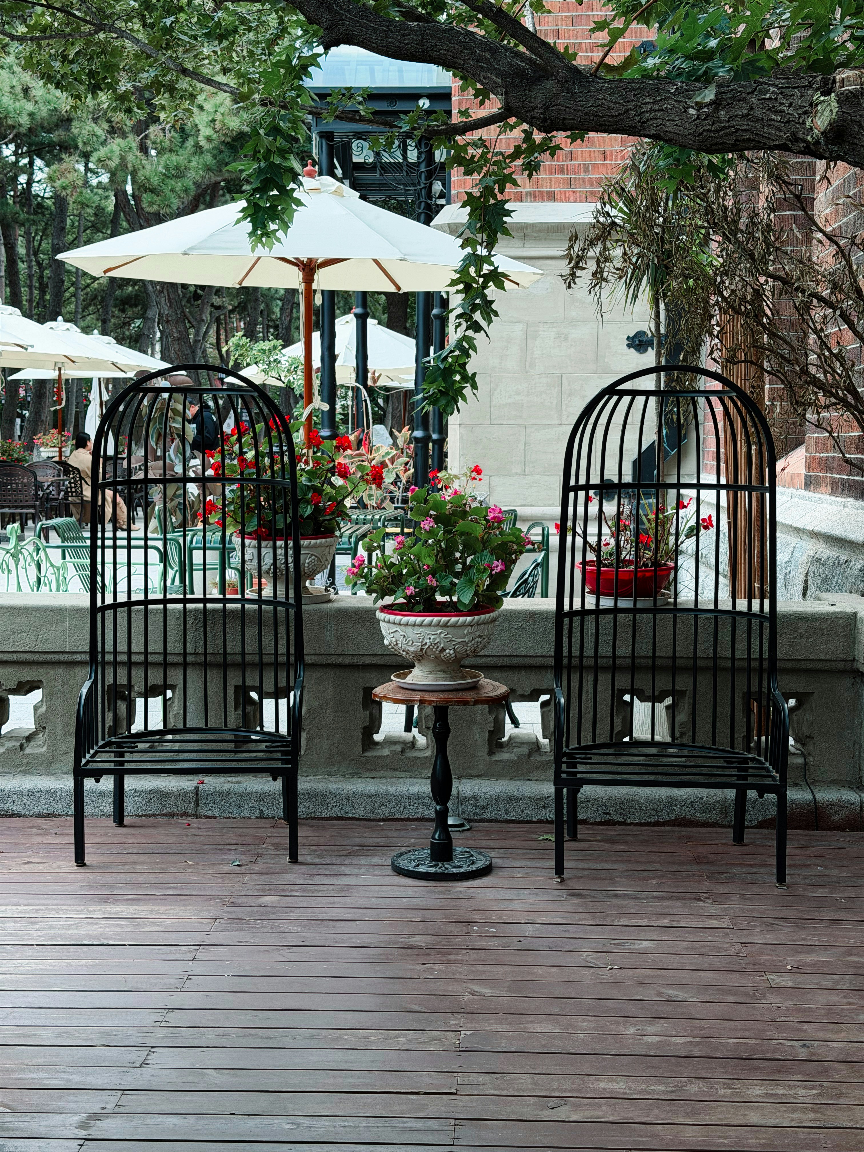 Two wrought-iron chairs face a flower-filled table on a sunny patio