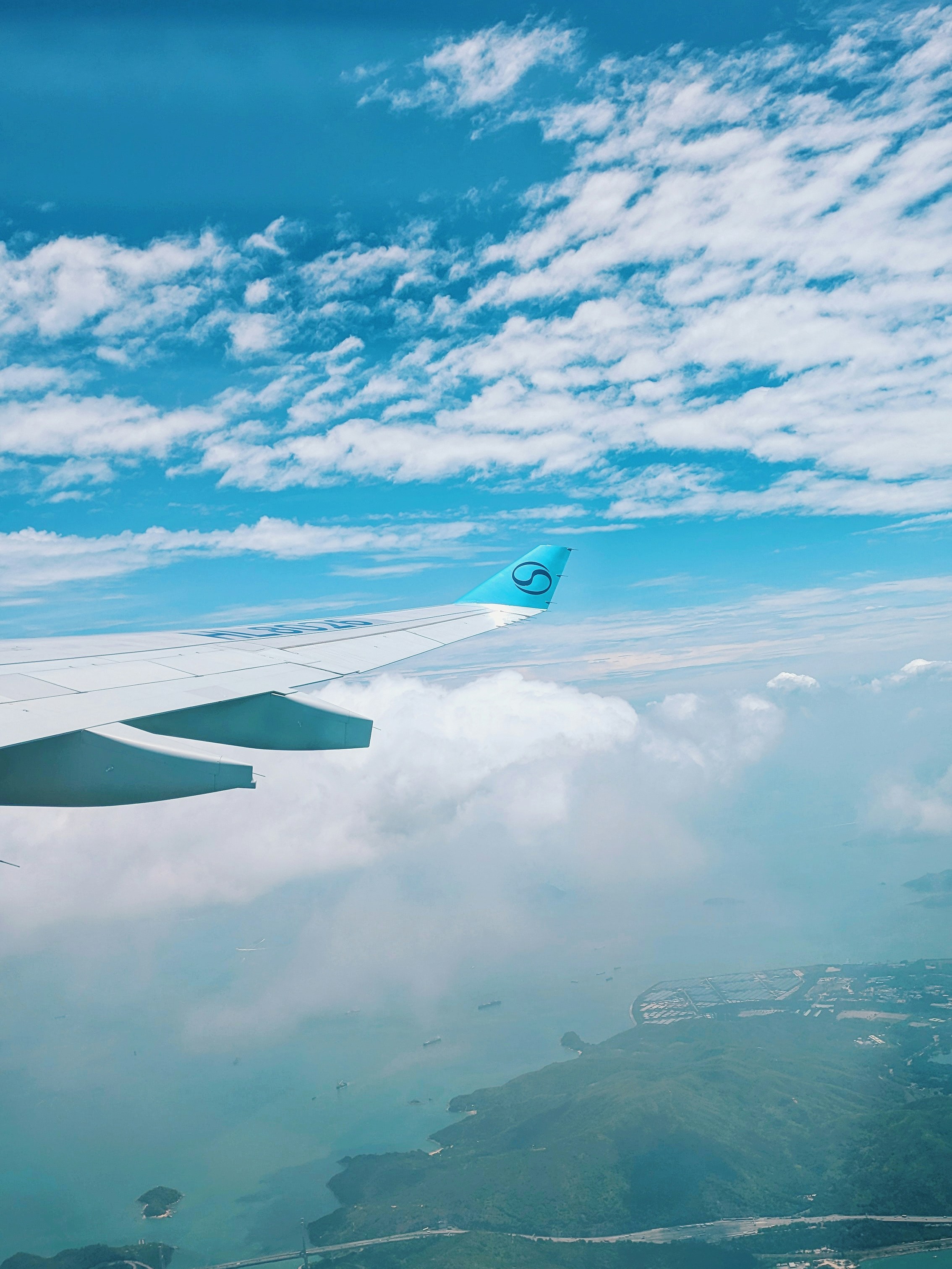 Airplane wing over coastal islands and bridges under a bright blue sky with scattered clouds – aerial view from a commercial flight