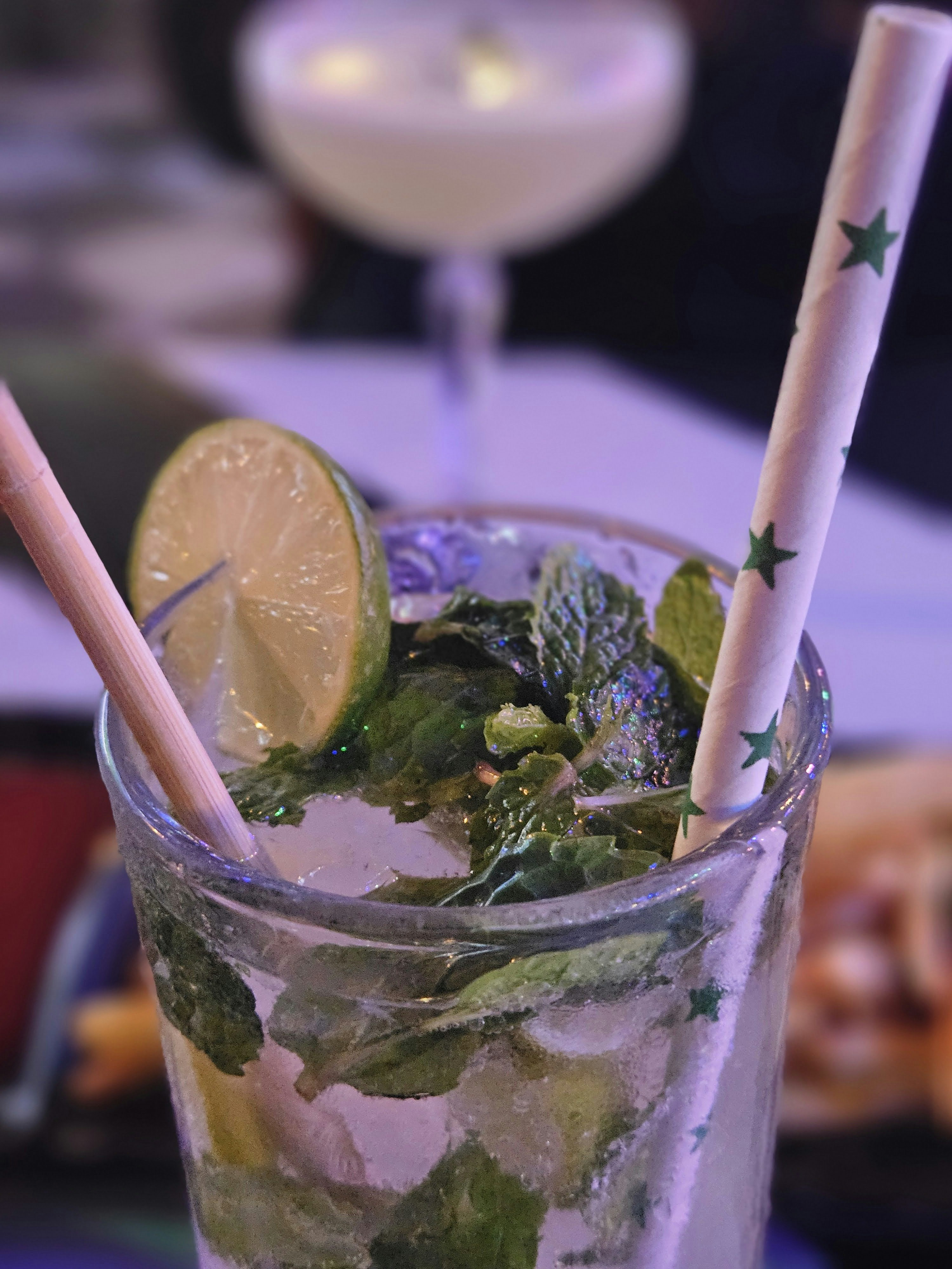 A mojito with mint leaves, lime, and star-patterned straws in a glass