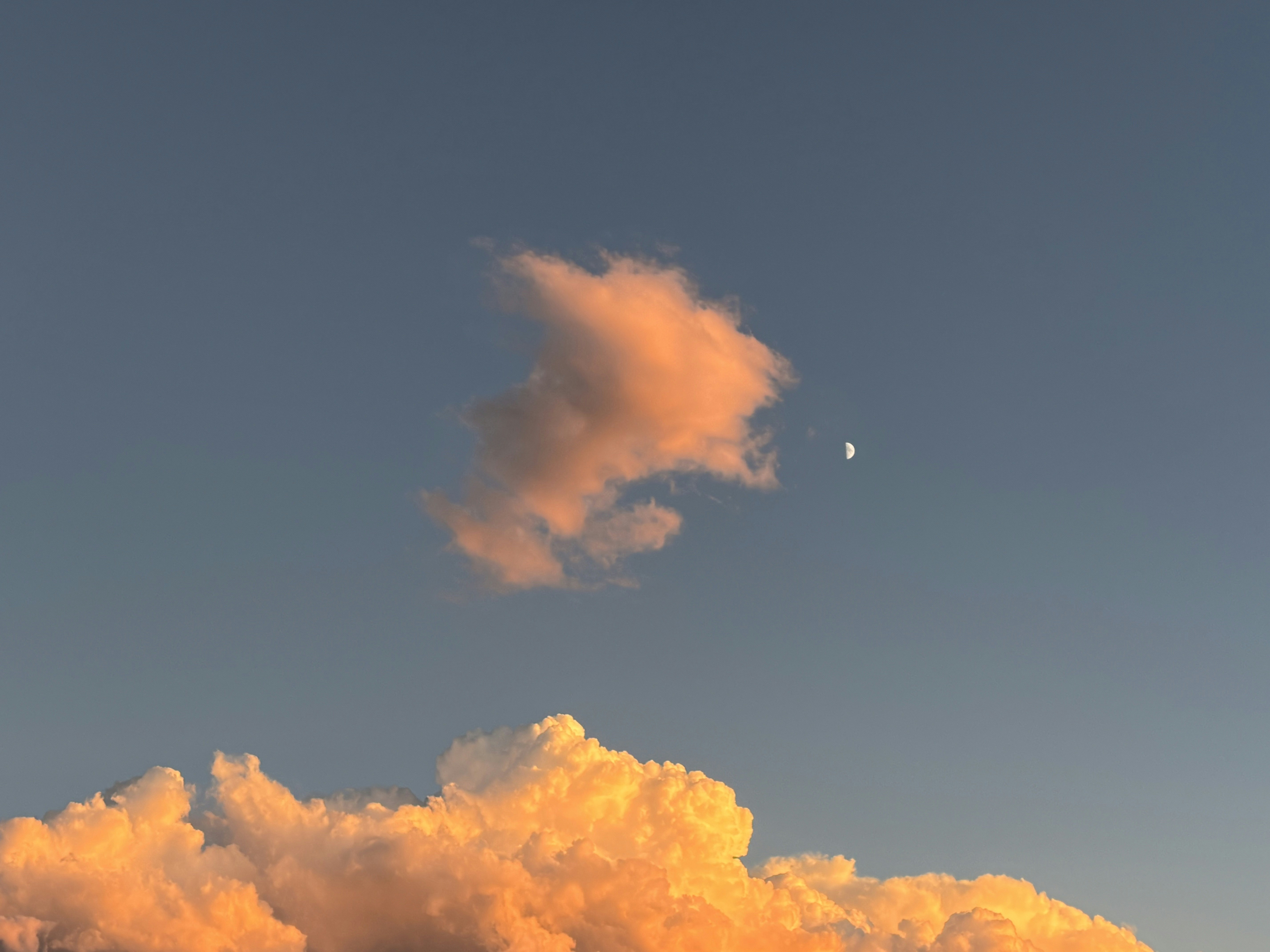A single orange cloud and a crescent moon in a clear blue sky
