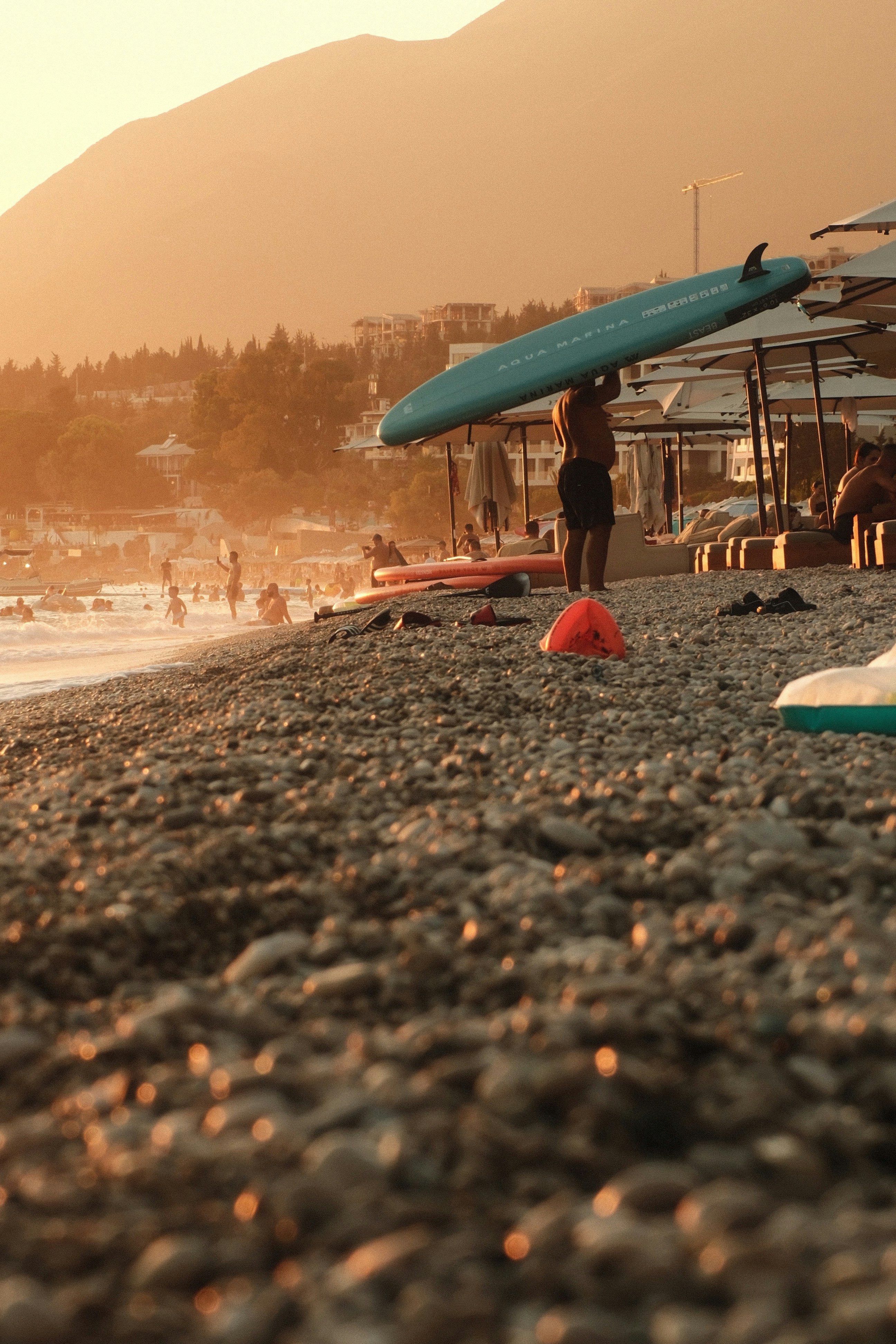 Sunset Surfers and Sunlit Pebbles on a Busy Beach