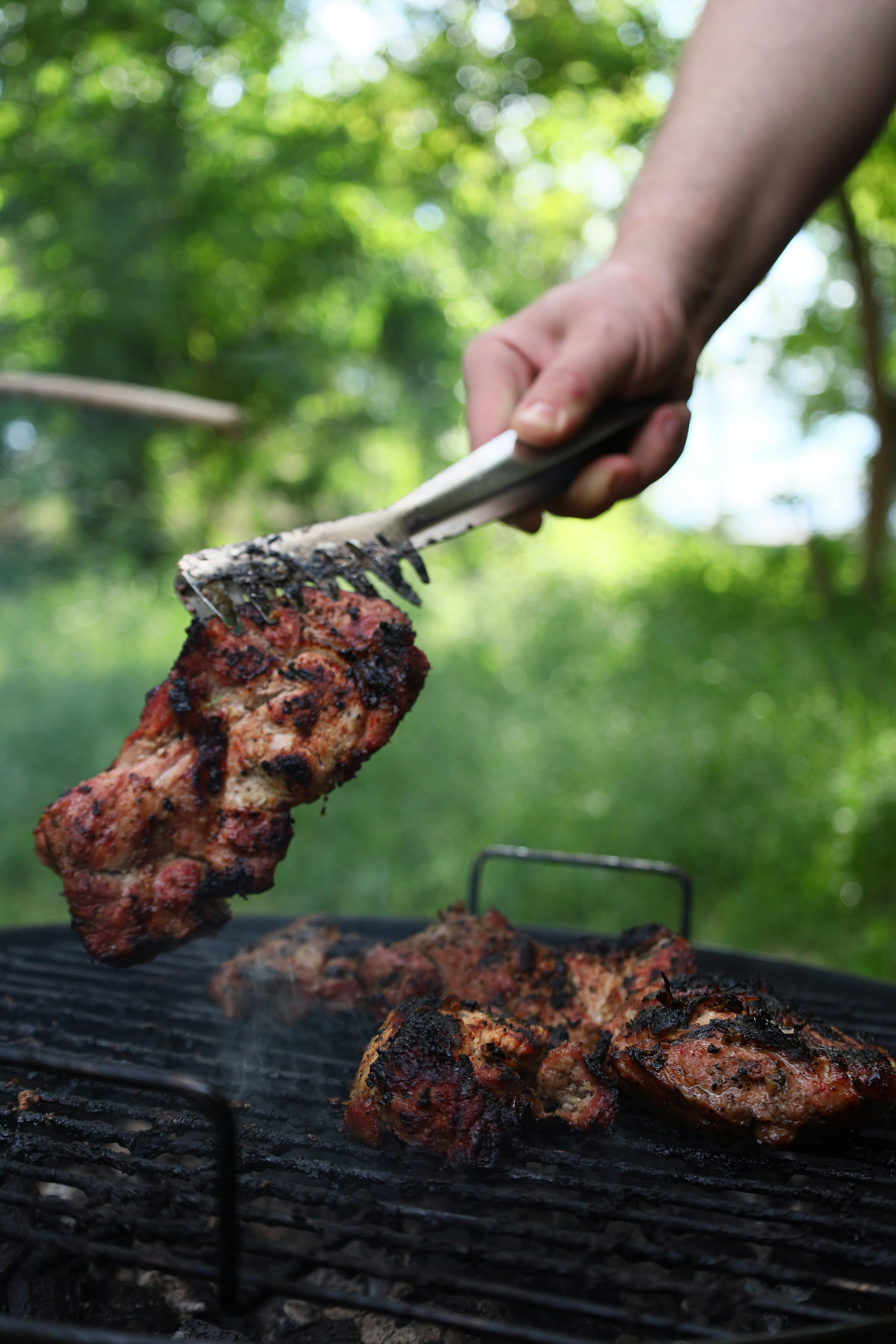 Grilled Moment: Tongs Lift a Charred Skewer Against a Luminous Outdoor Grill
