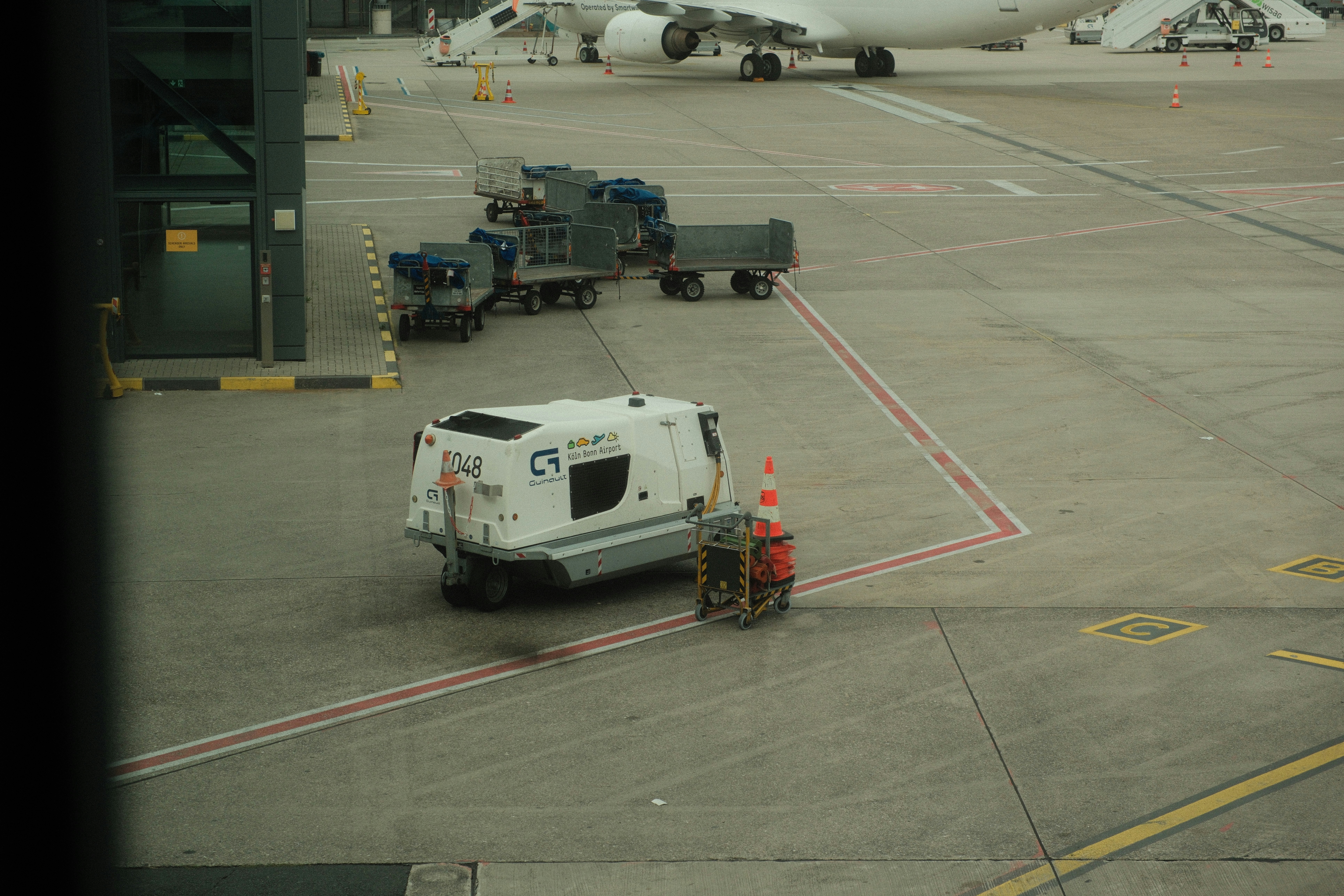 A white ground power unit and luggage carts on the tarmac at Cologne Bonn Airport