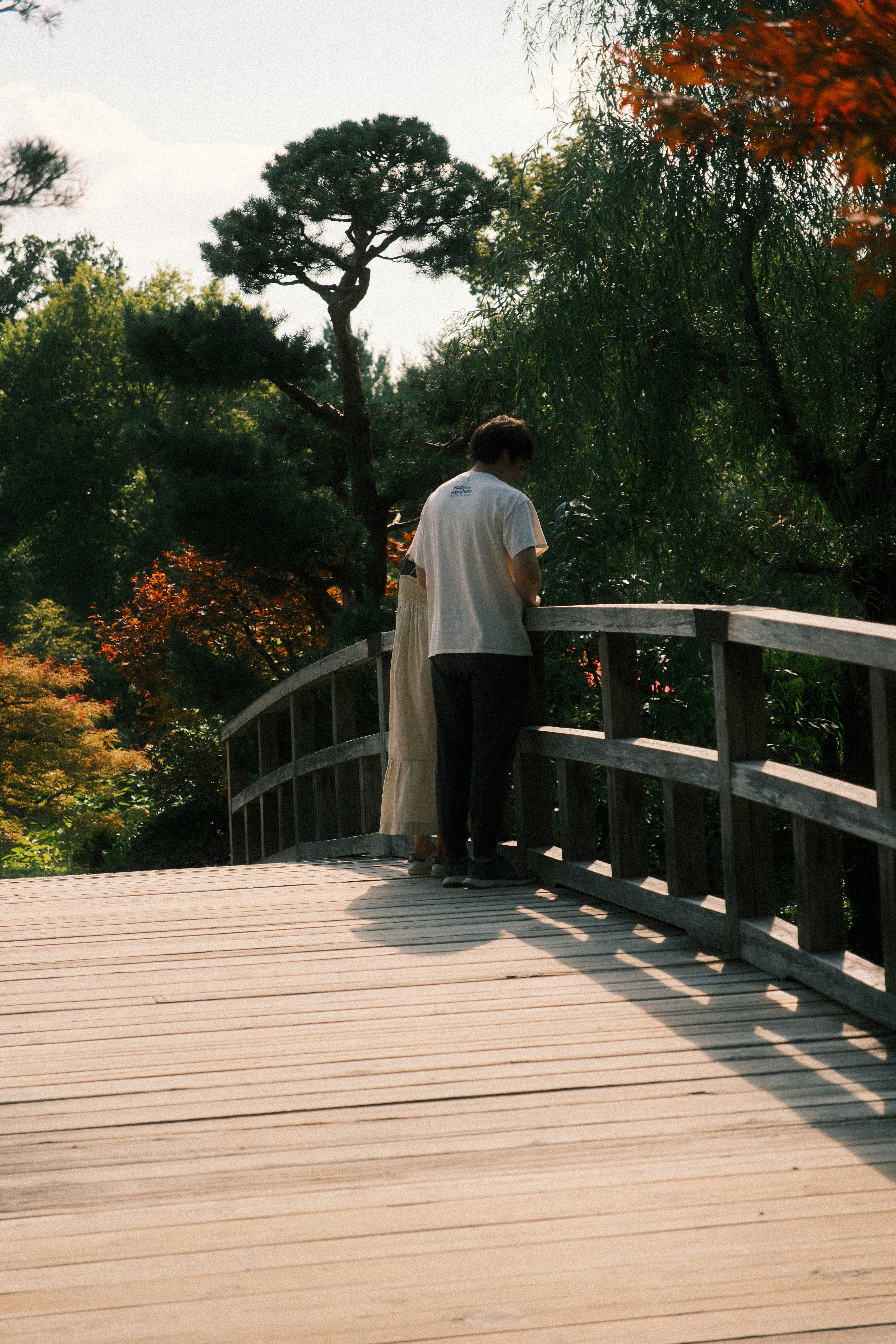 Couple on a sunlit wooden bridge amidst autumn-hued trees