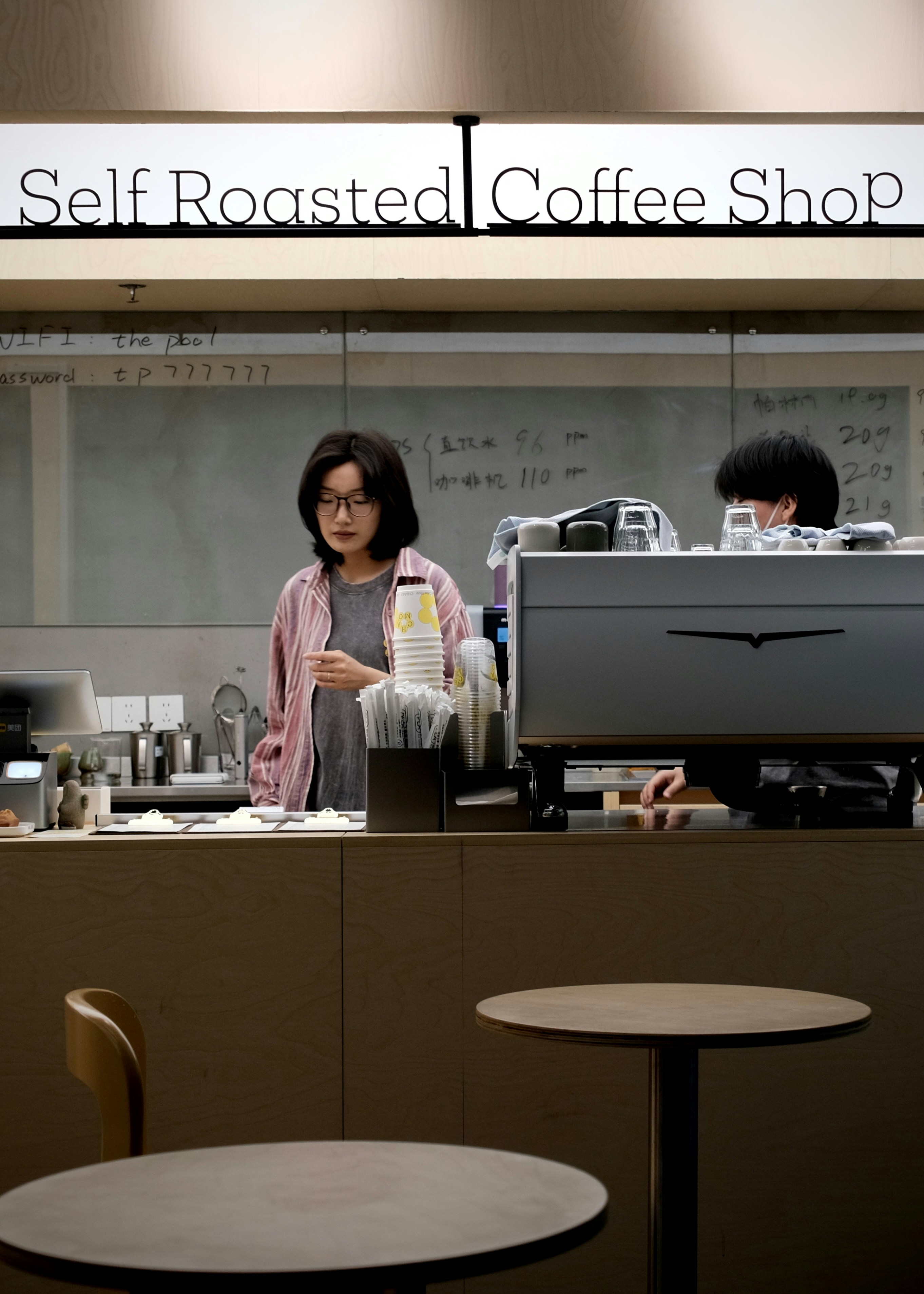 A woman standing behind a counter in a coffee shop with a chalkboard wall