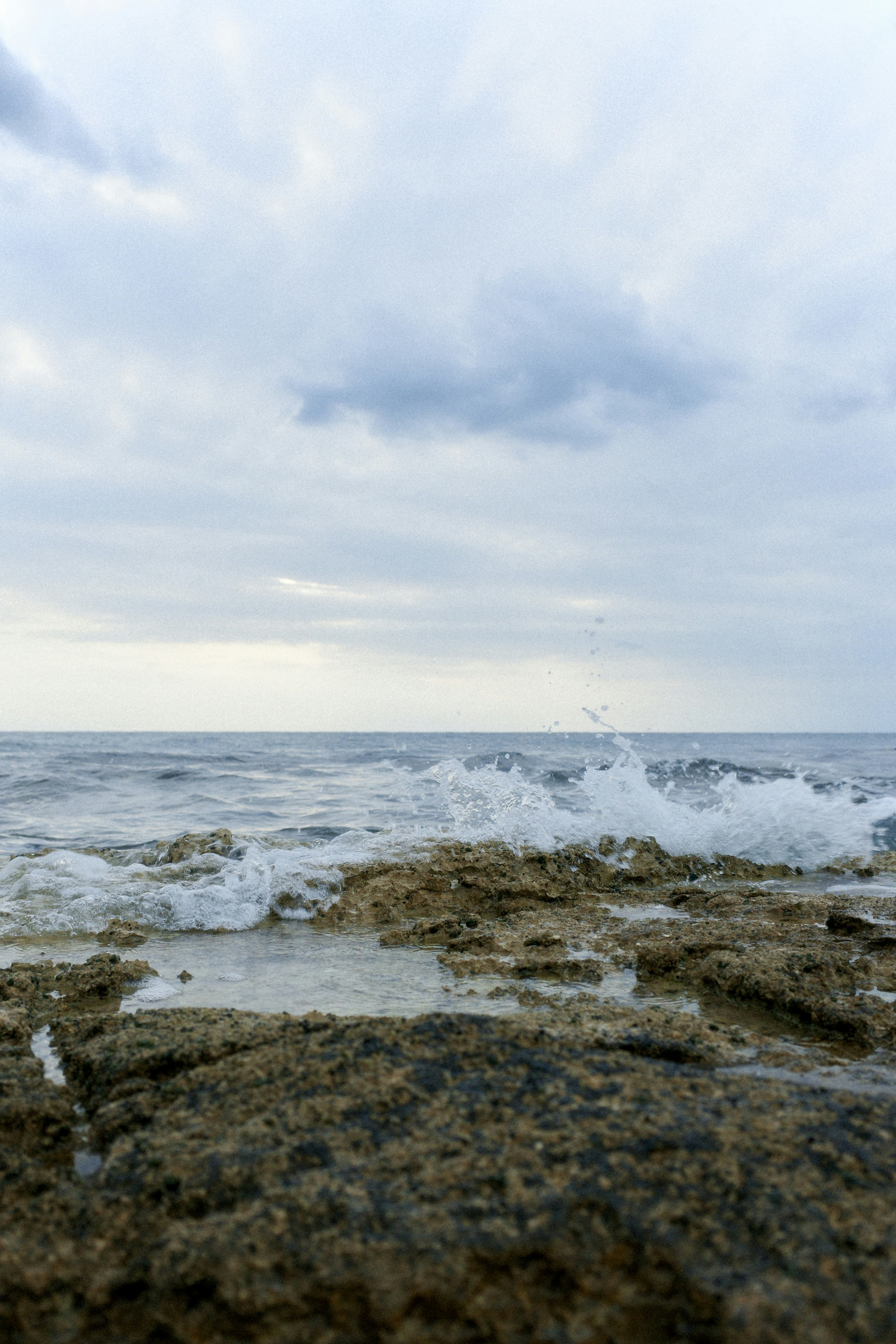 Rugged shoreline with waves crashing against rock, horizon meeting a pale sky; a minimal seascape highlighting texture and movement.