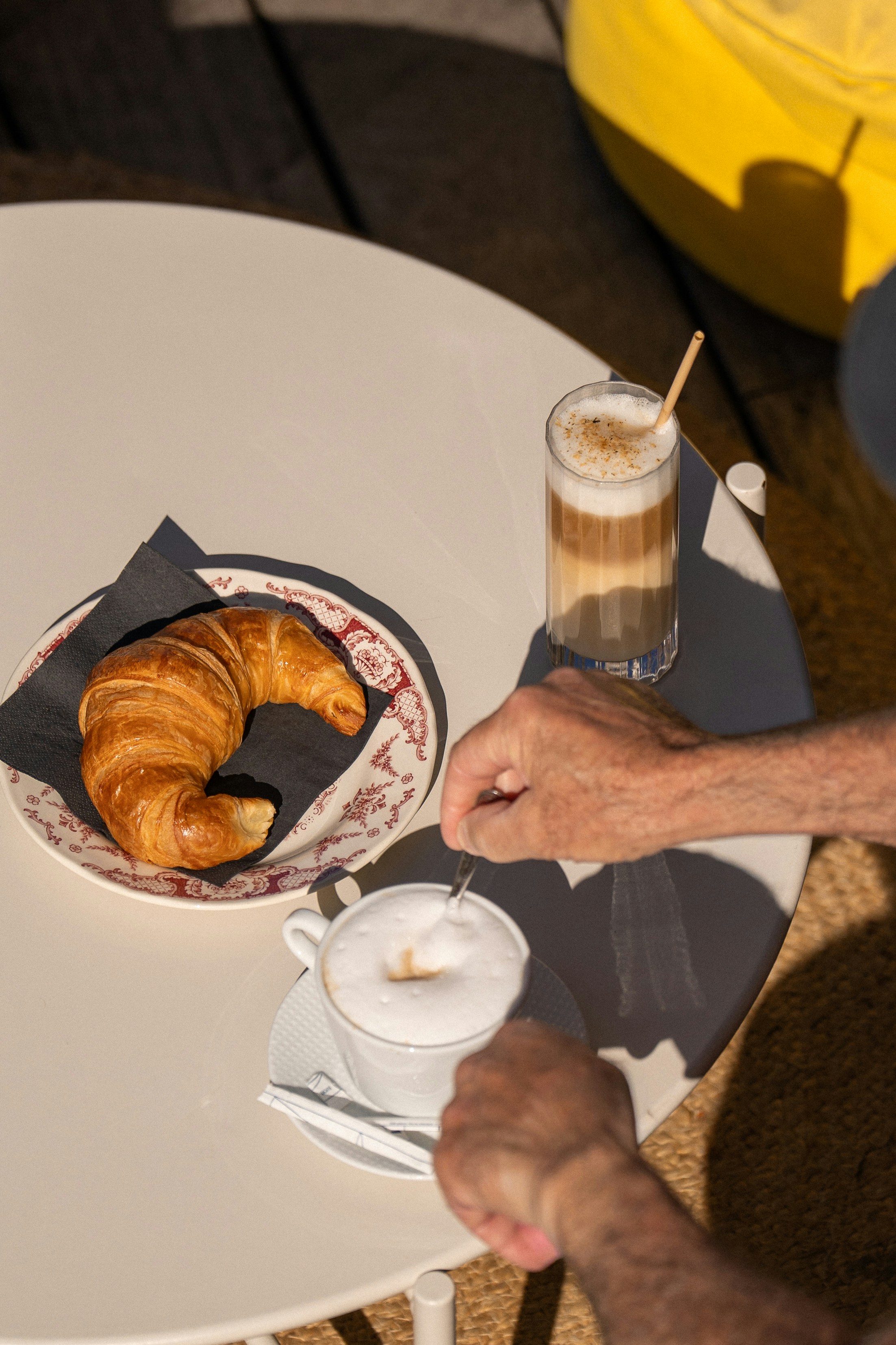Cafe Stop: A Croissant, Foam, and Two Hands on a Sunlit Table