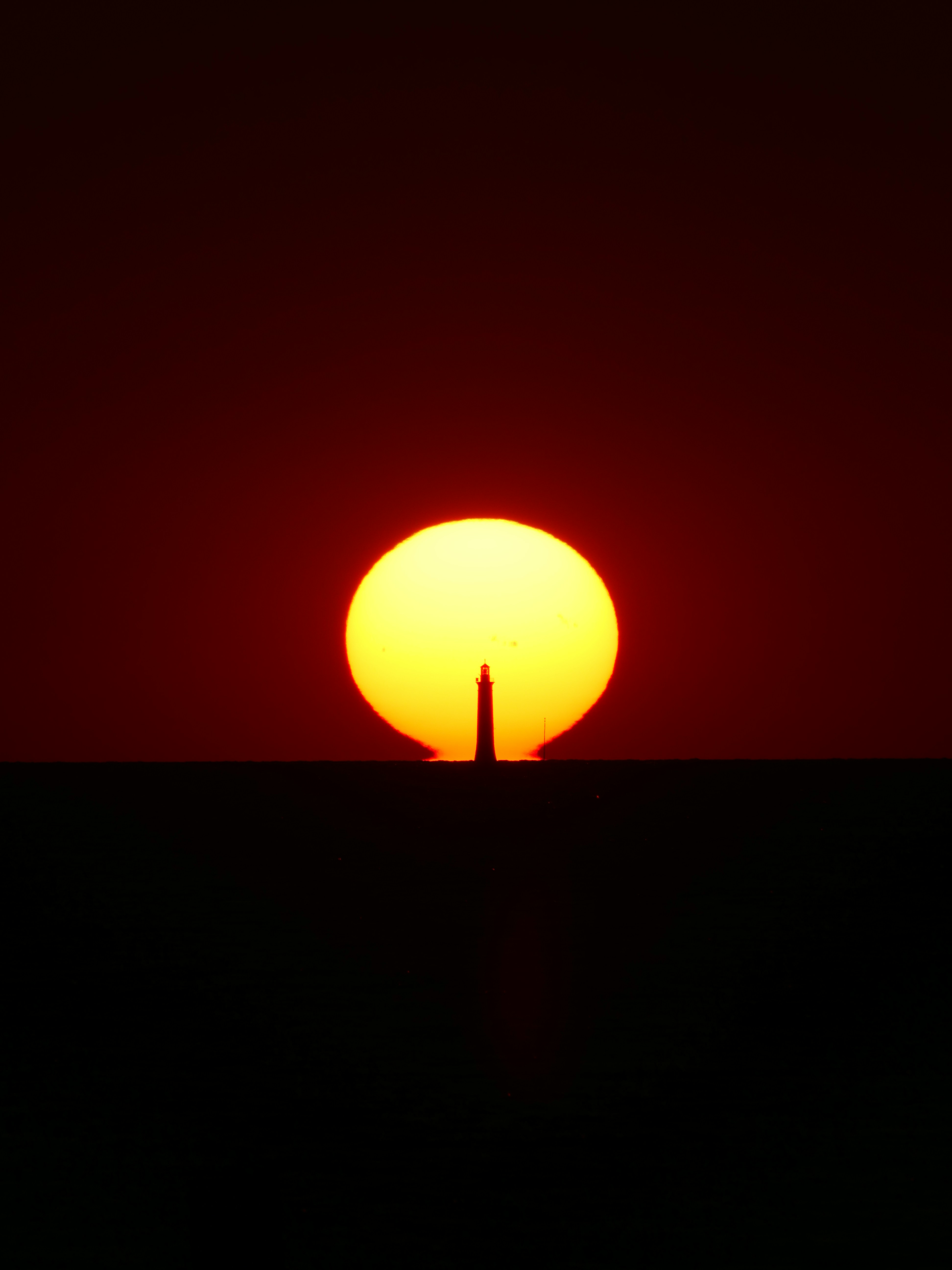 Sunrise Sentinel: The Lighthouse Silhouette Against a Crimson Horizon
