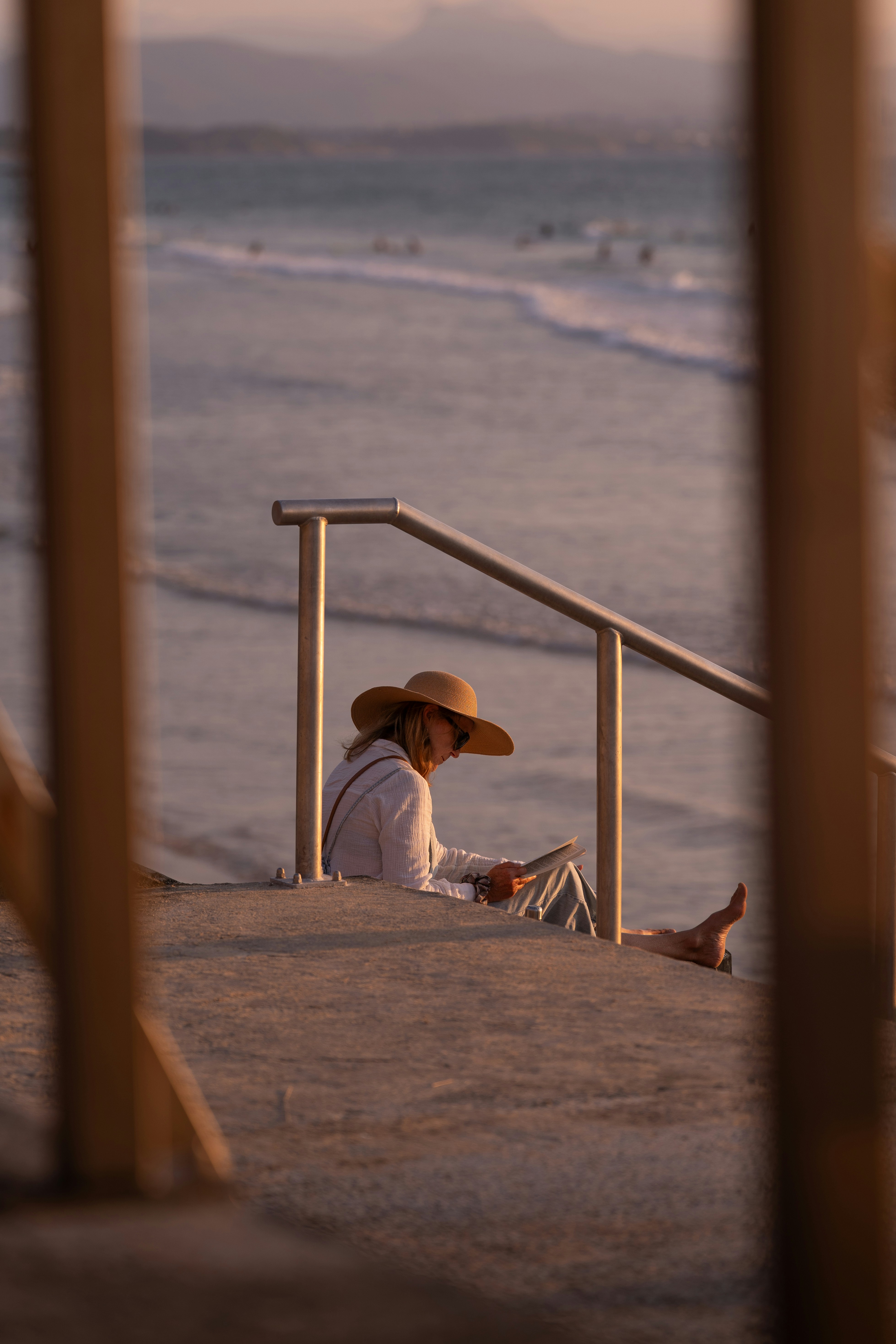 Woman reading by the Atlantic Ocean in the warm evening light on the Côte des Basques in Biarritz, France.