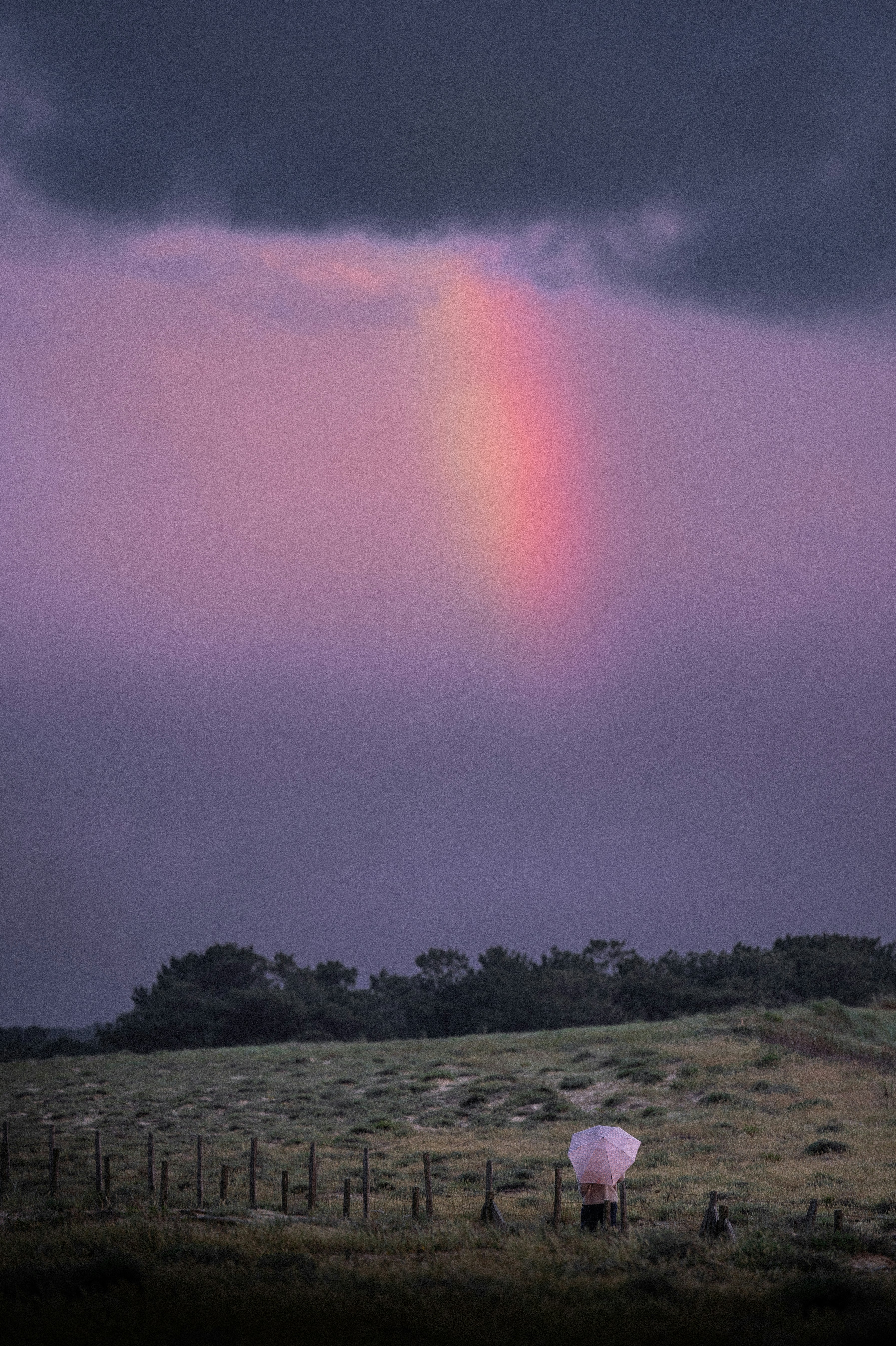 Rainbow over a Quiet Field: A lone figure with an umbrella