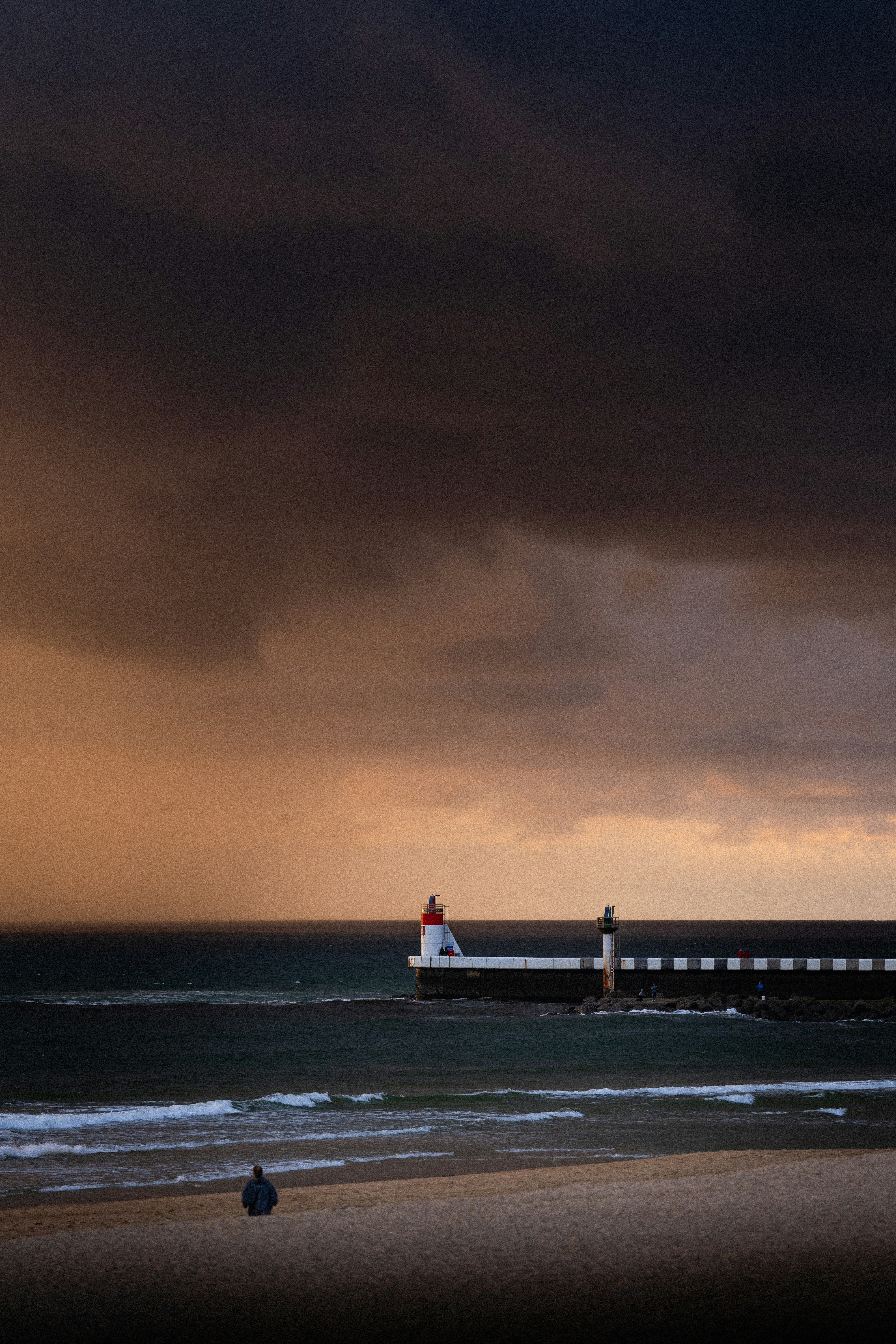 Stormy Sunset by the Pier: Lone Figure on the Quiet Beach