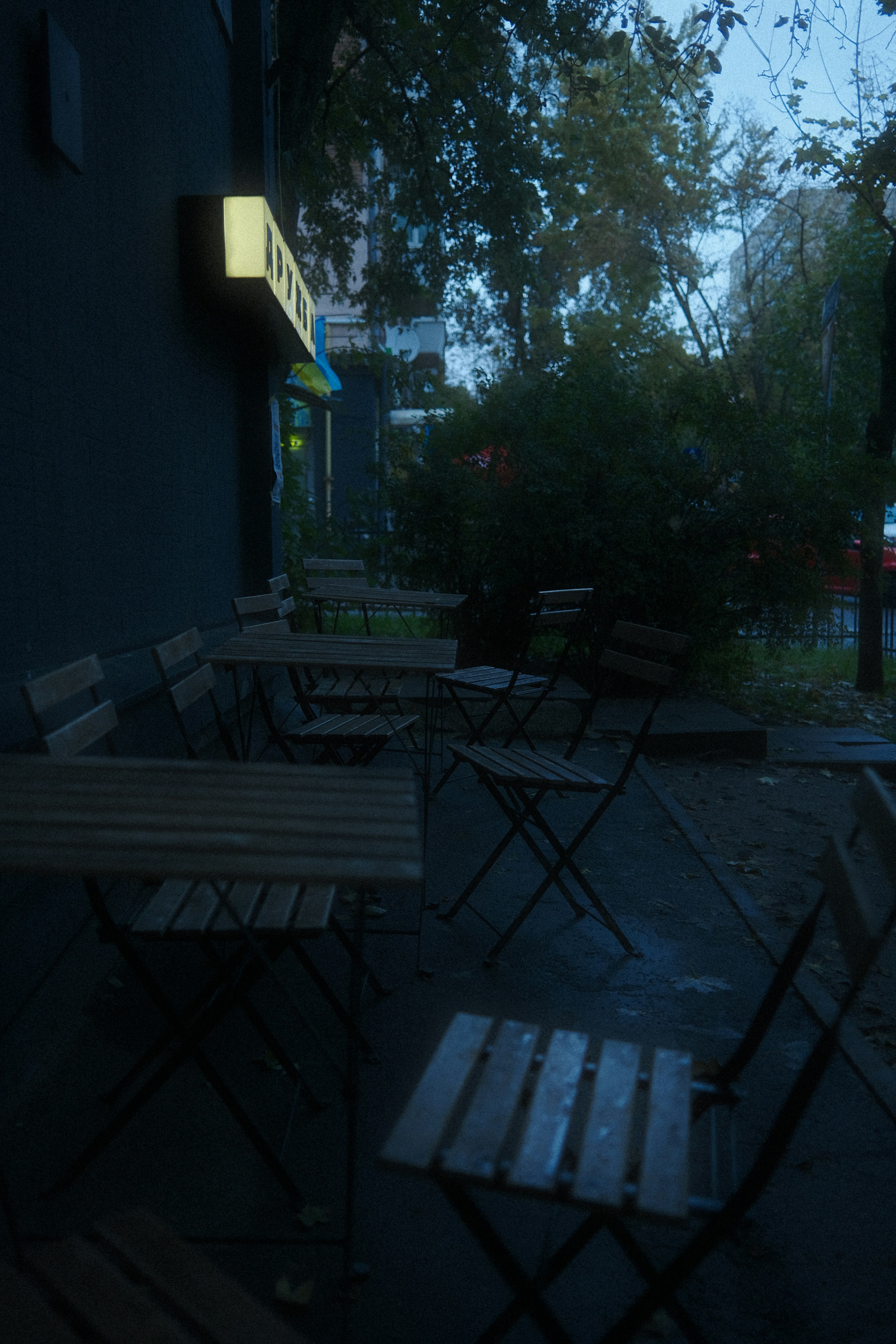 Empty wooden tables and chairs on a dark patio outside a cafe