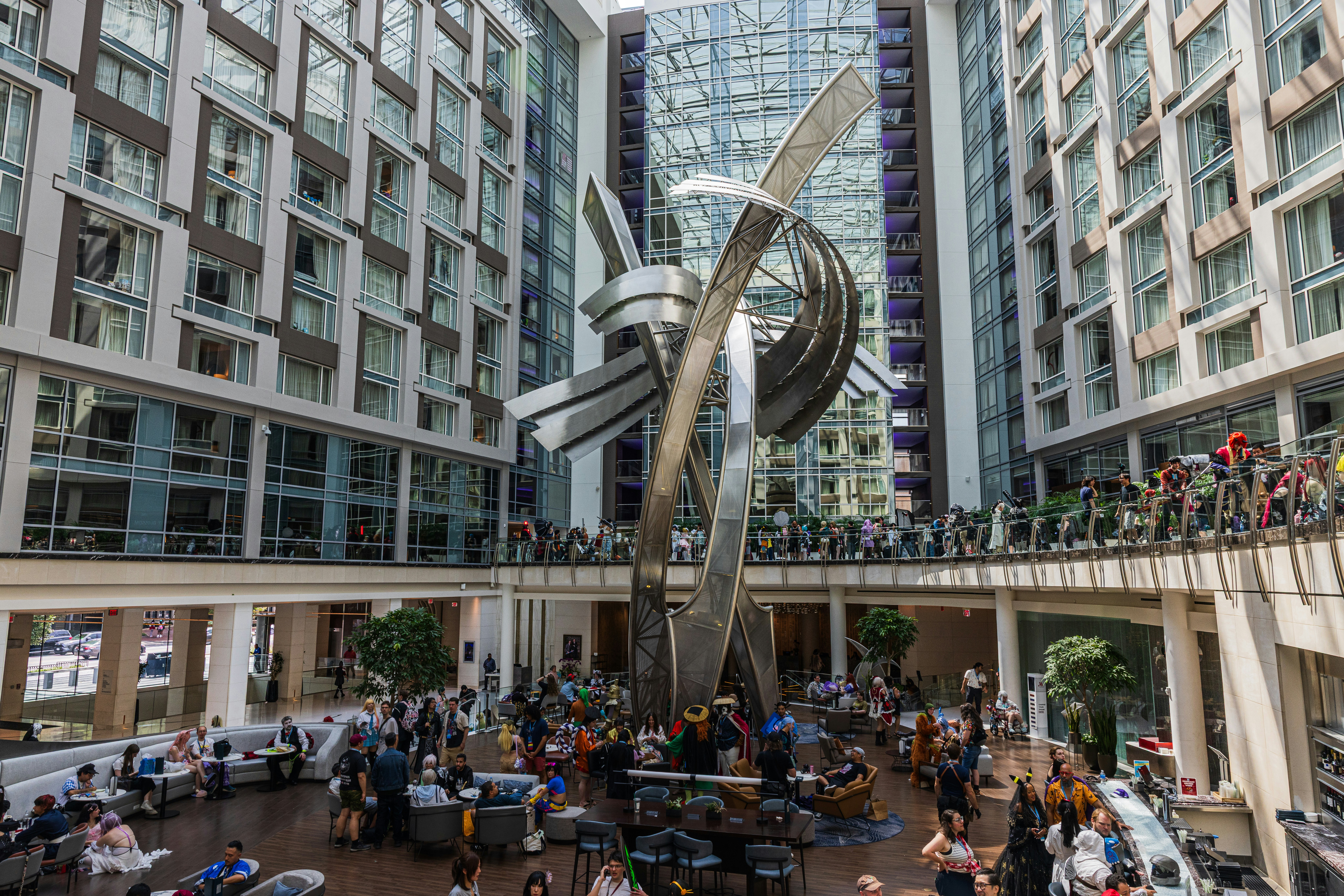 An expansive atrium of a modern hotel features a large metallic sculpture surrounded by multiple floors of windows and balconies.