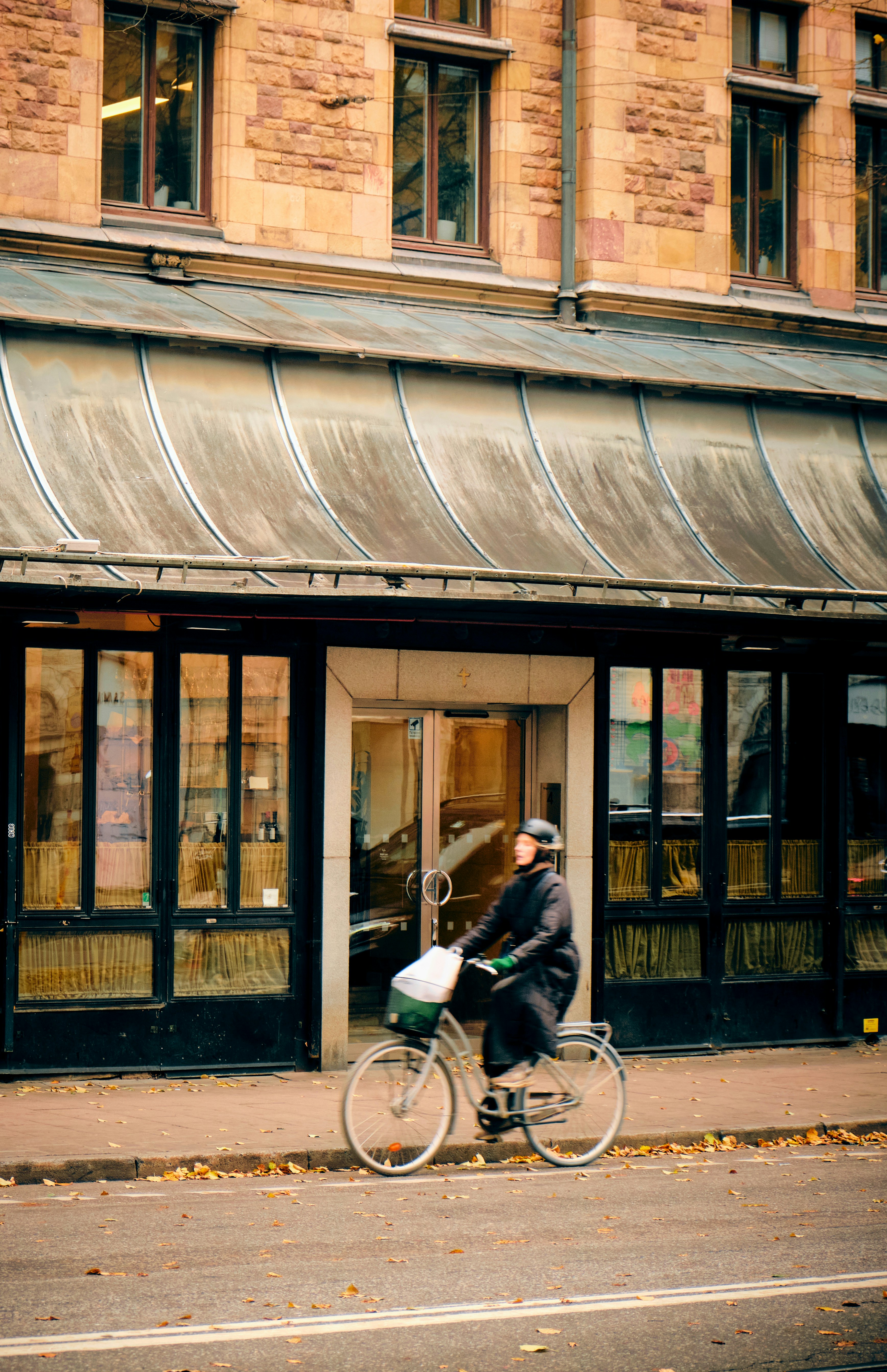 A person in a dark coat and helmet cycling past a building with large windows