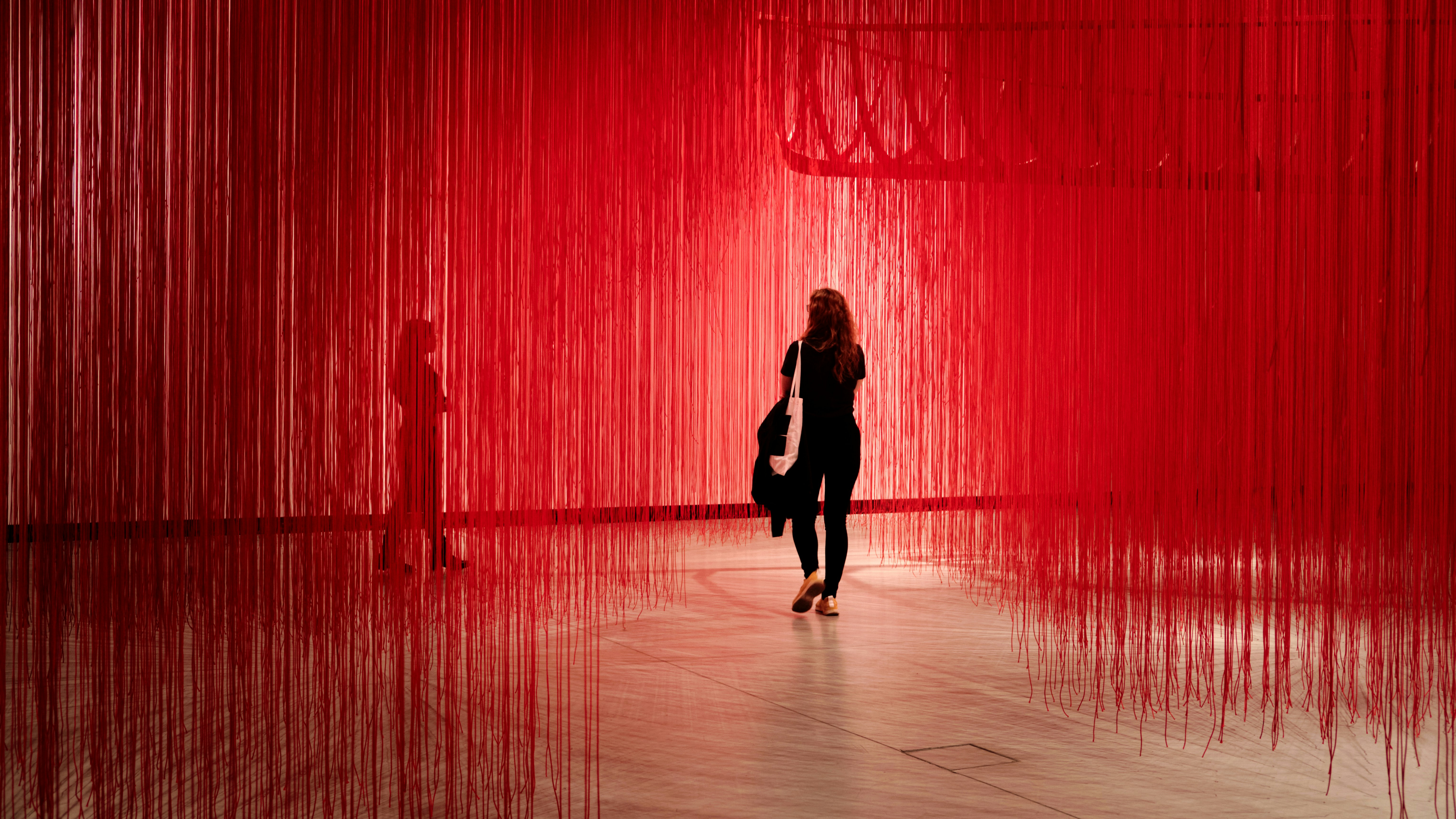 Red Corridor of Echoes: A Woman Walks Between Strings of Light