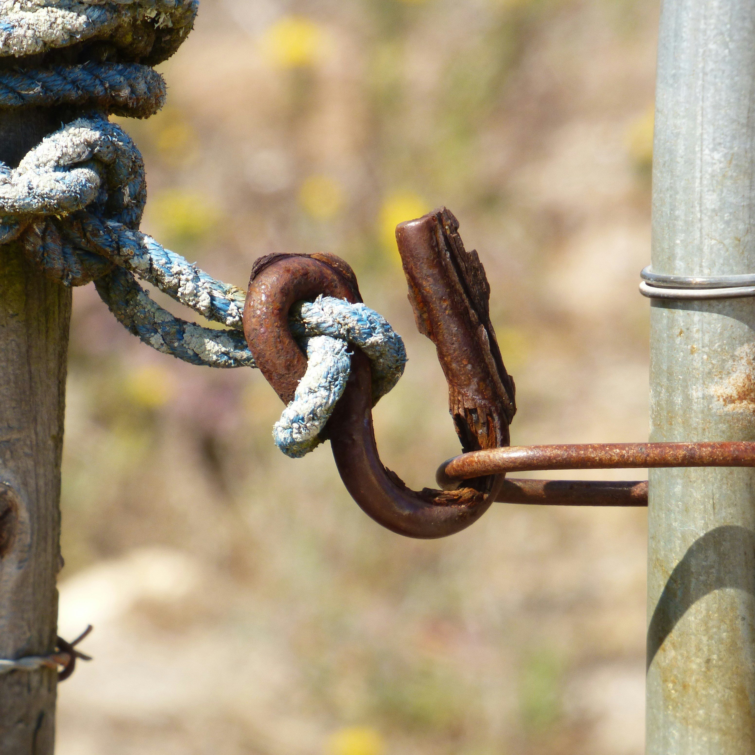 A weathered blue rope tied to a rusty metal hook on a fence