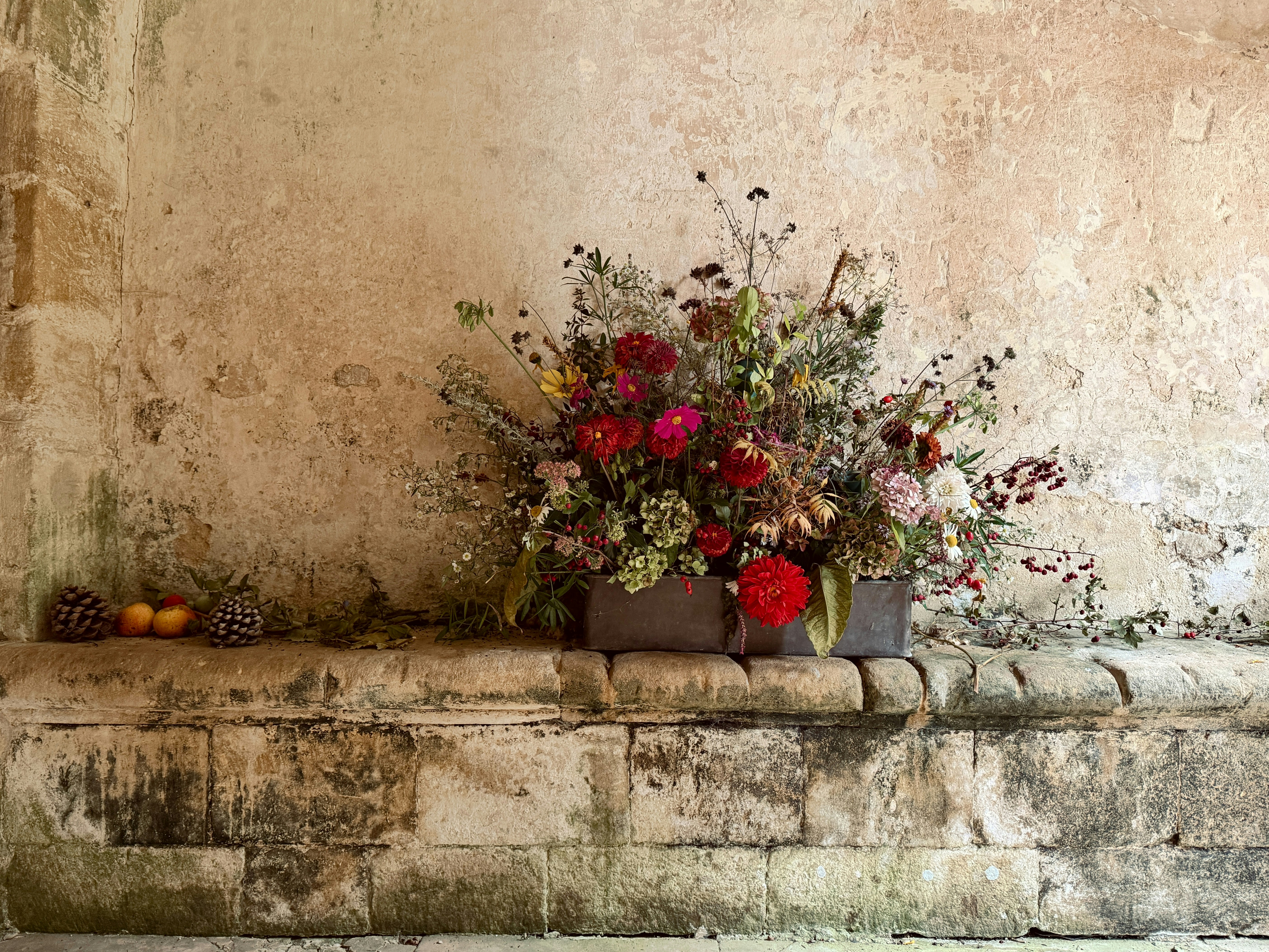 A large floral arrangement in metal containers on a weathered stone ledge