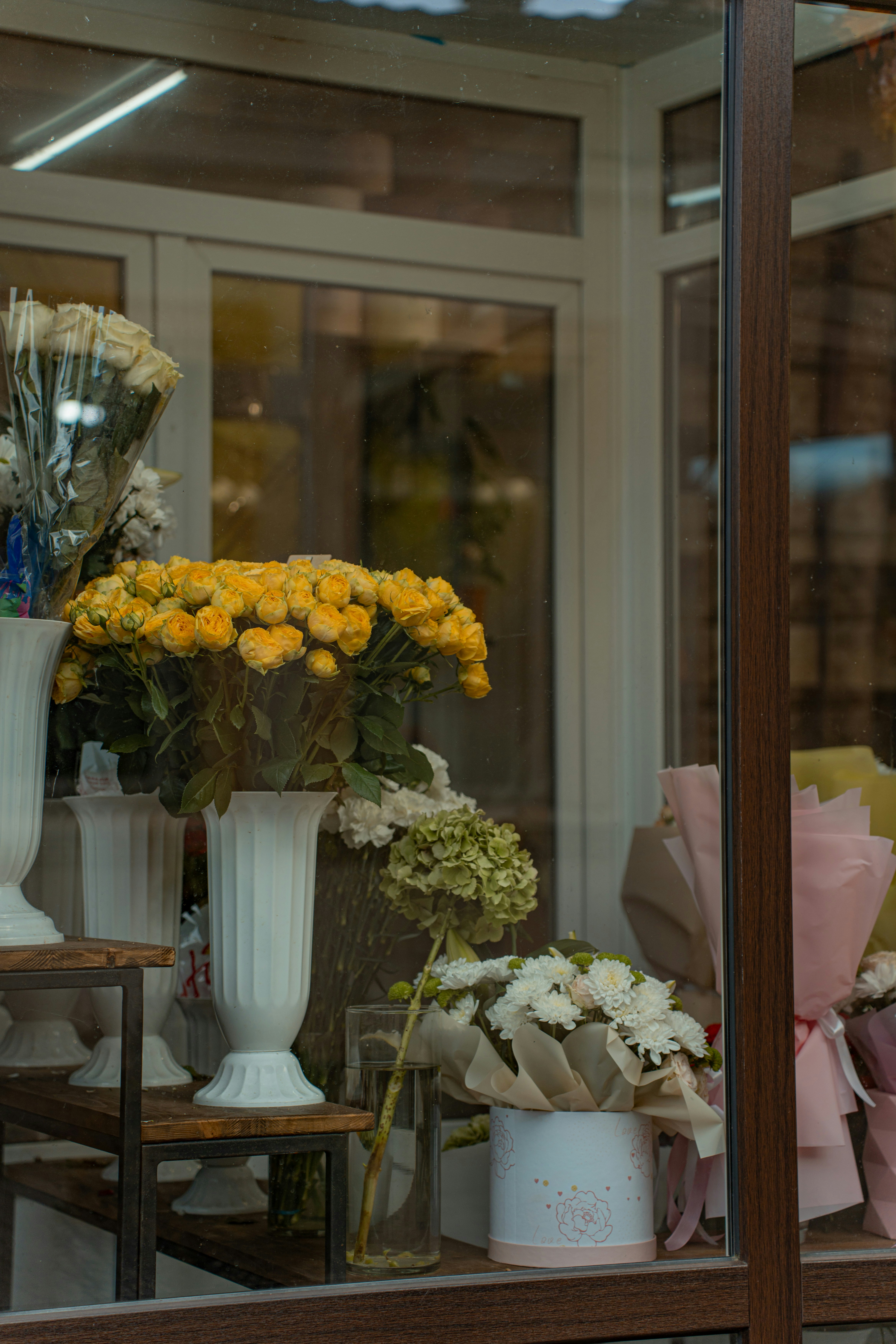 Yellow roses in a white vase inside a flower shop window display