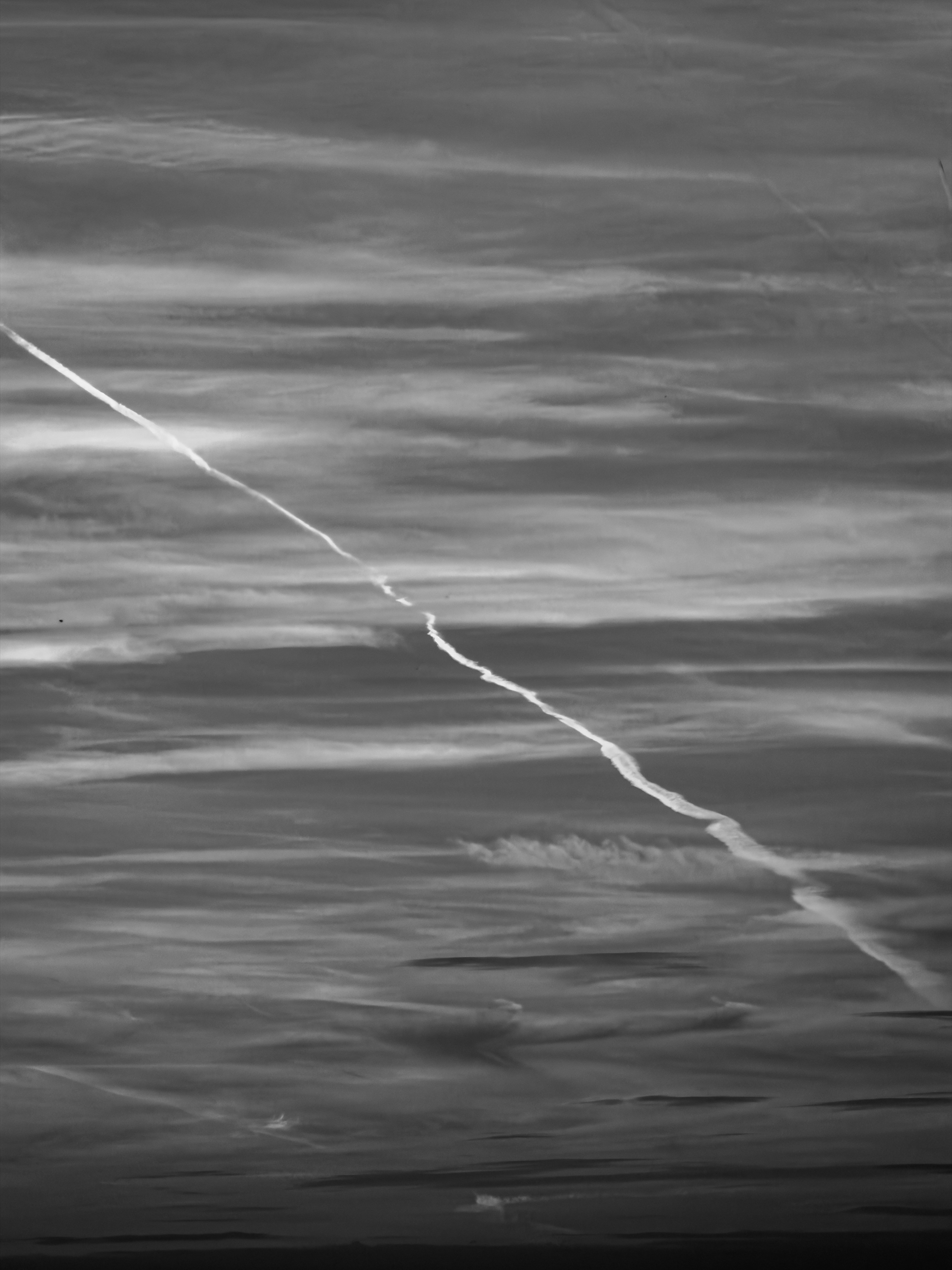 A single white contrail cutting across a dark, cloudy sky