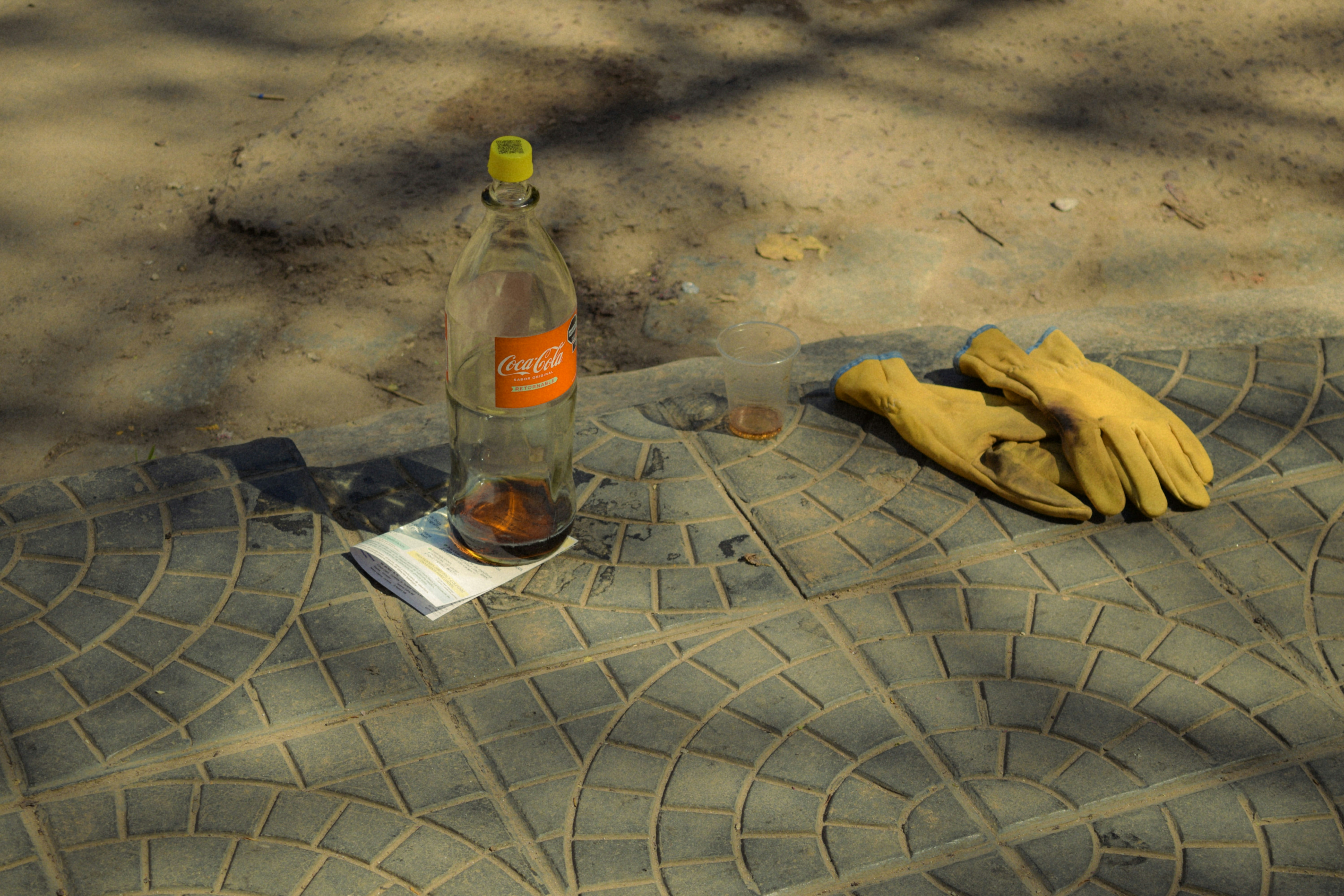 Glass soda bottle and yellow work gloves sitting on pavement