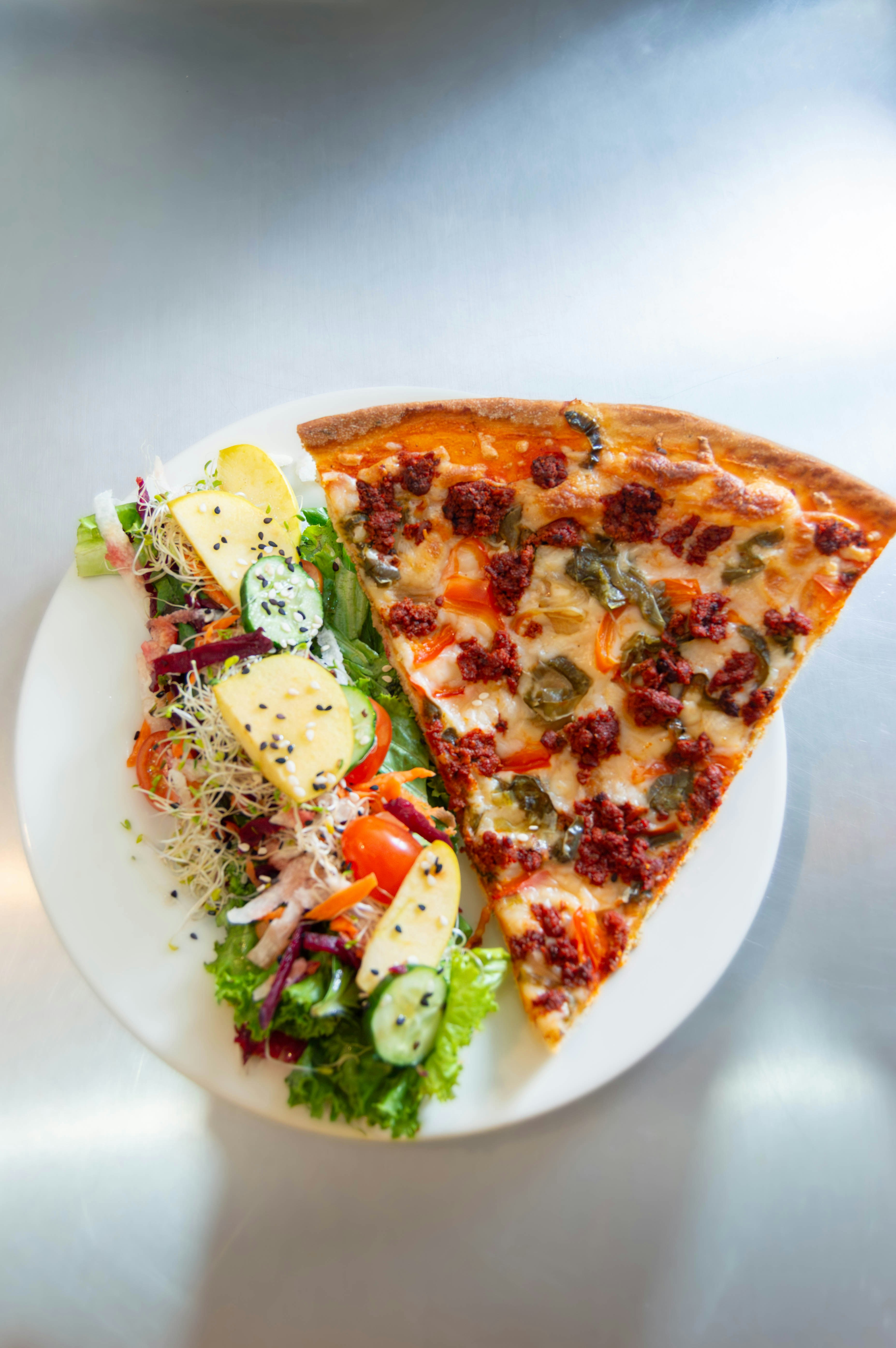 A slice of chorizo pizza beside a fresh garden salad on a white plate
