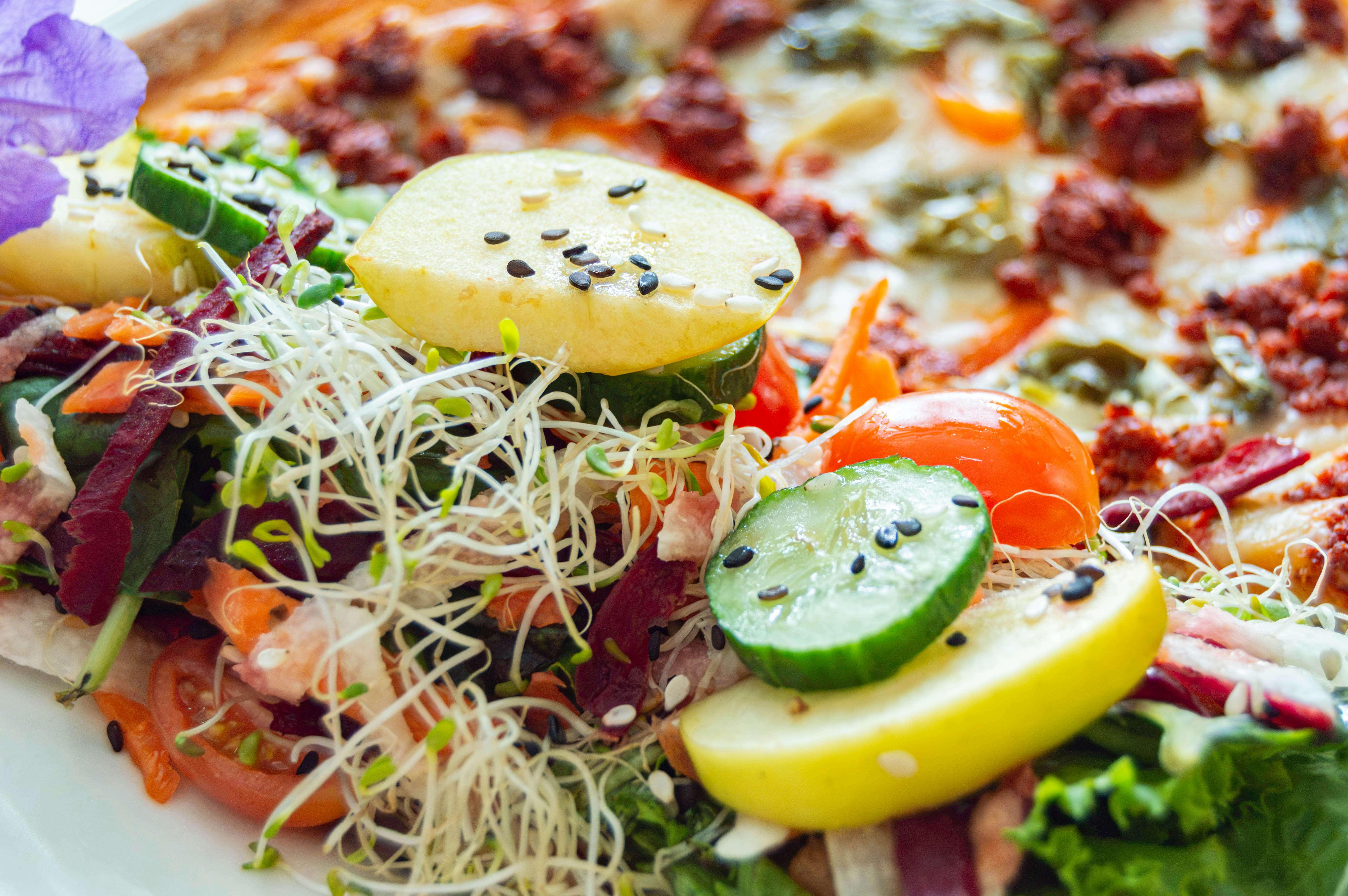 Bright, colorful veggie pizza featuring leafy greens, sprouts, and cucumber-slice toppings on a cheesy base.