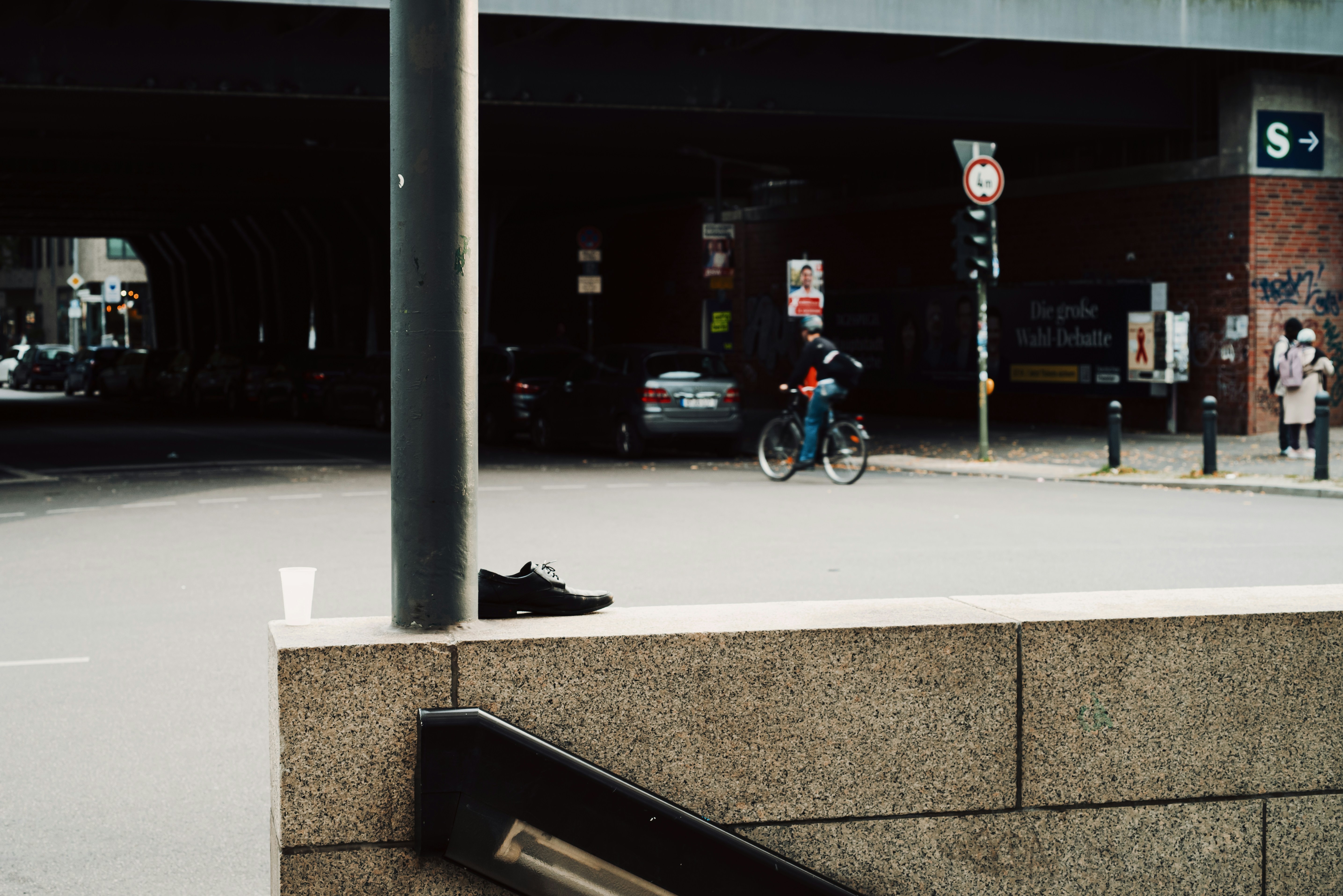 Concrete ledge, lone shoe, and distant cyclist under an urban overpass