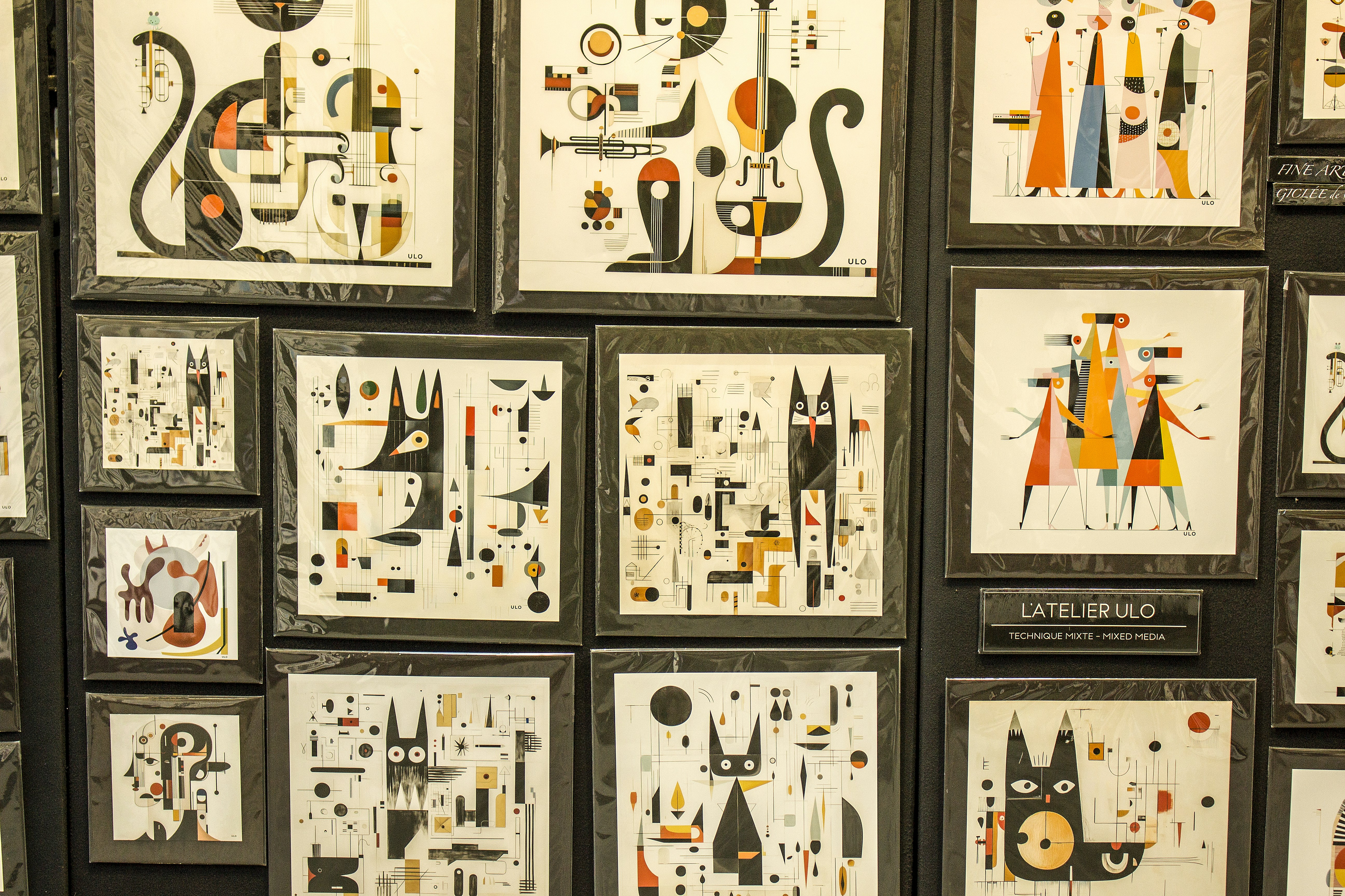 Clustered abstract art frames featuring geometric shapes and cat silhouettes arranged on a gallery wall.