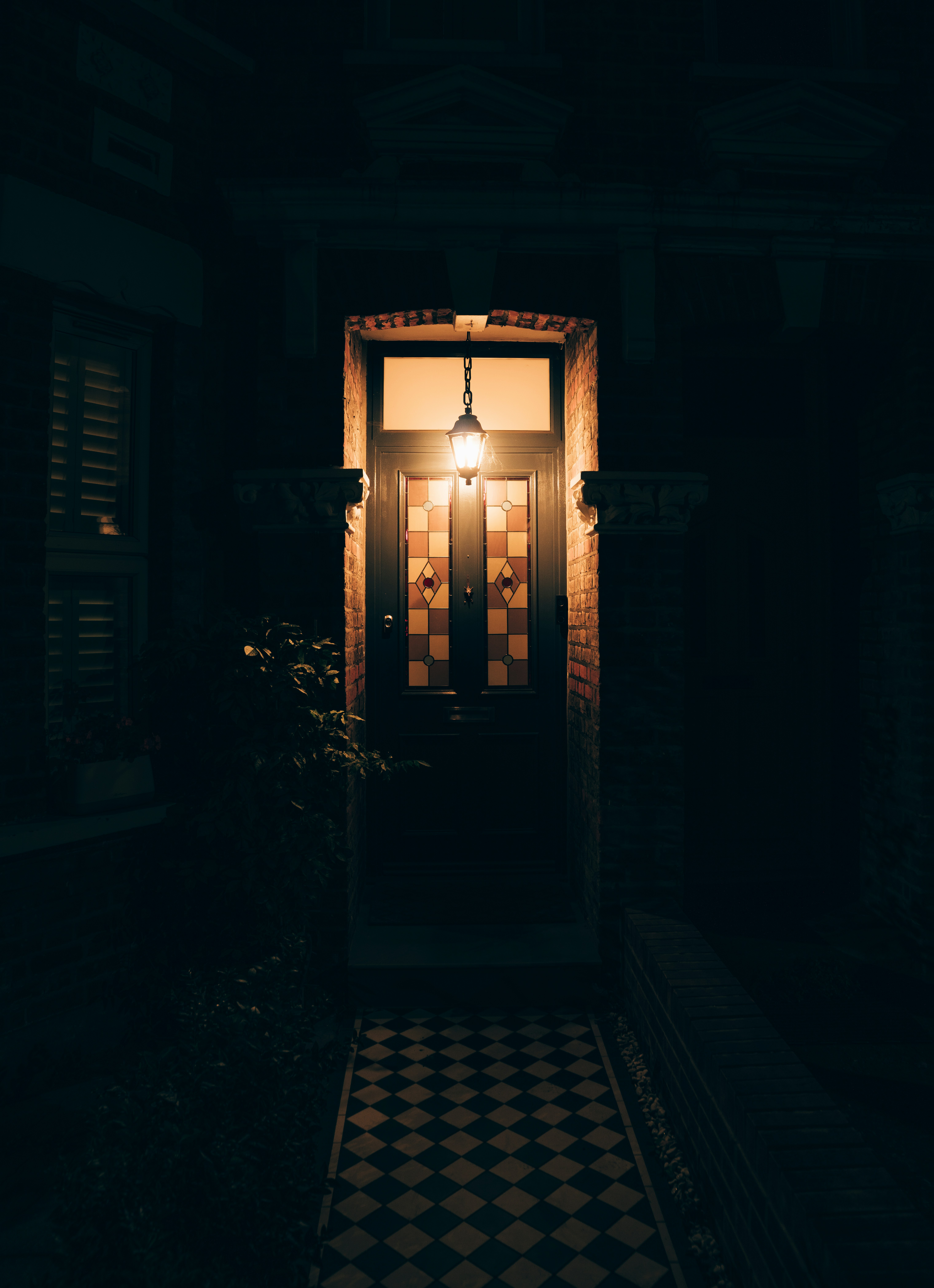 A dark front door with stained glass panels illuminated by a hanging lantern