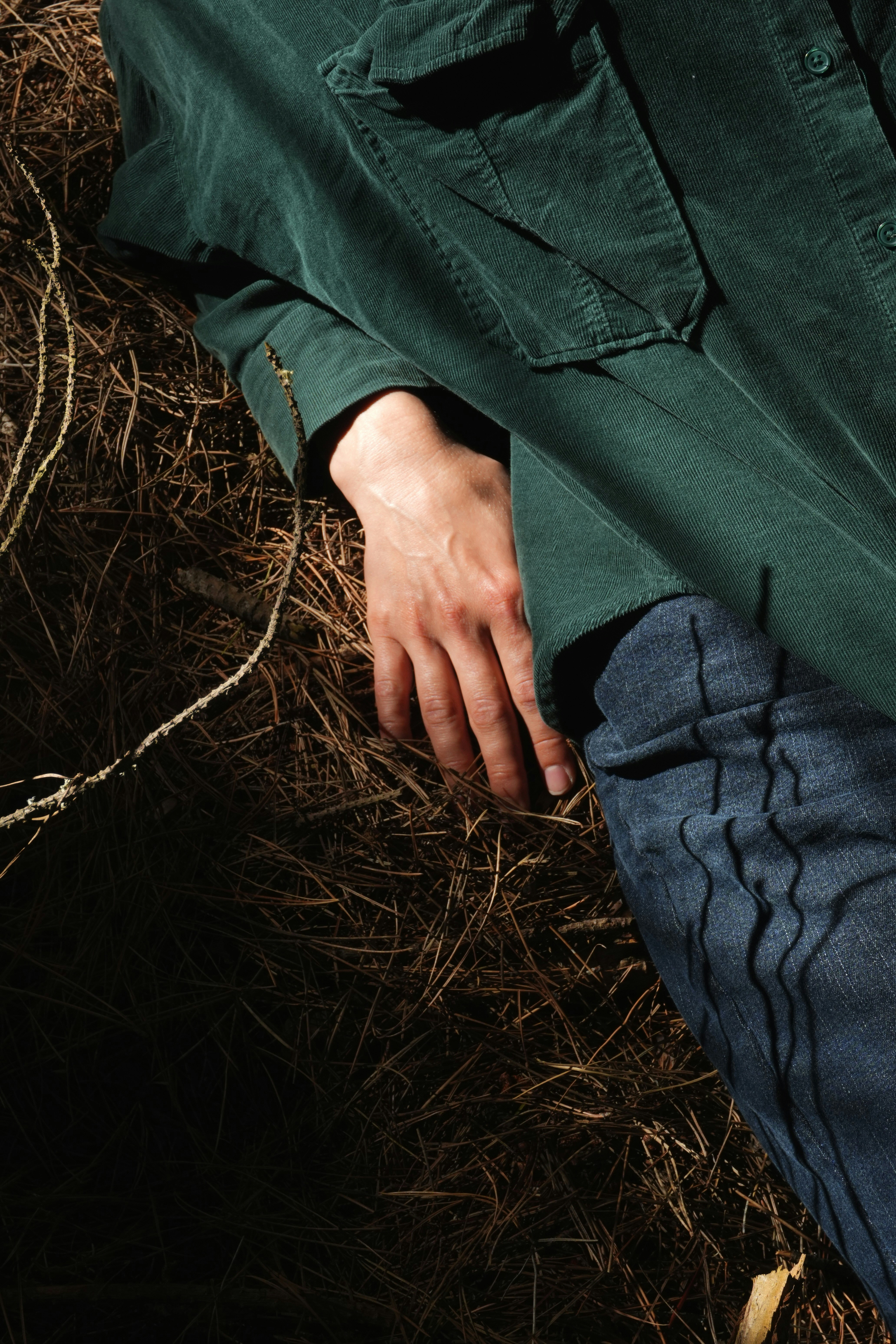 Outstretched Hand in Dark-Textured Green Shirt Against Pine Needle Ground