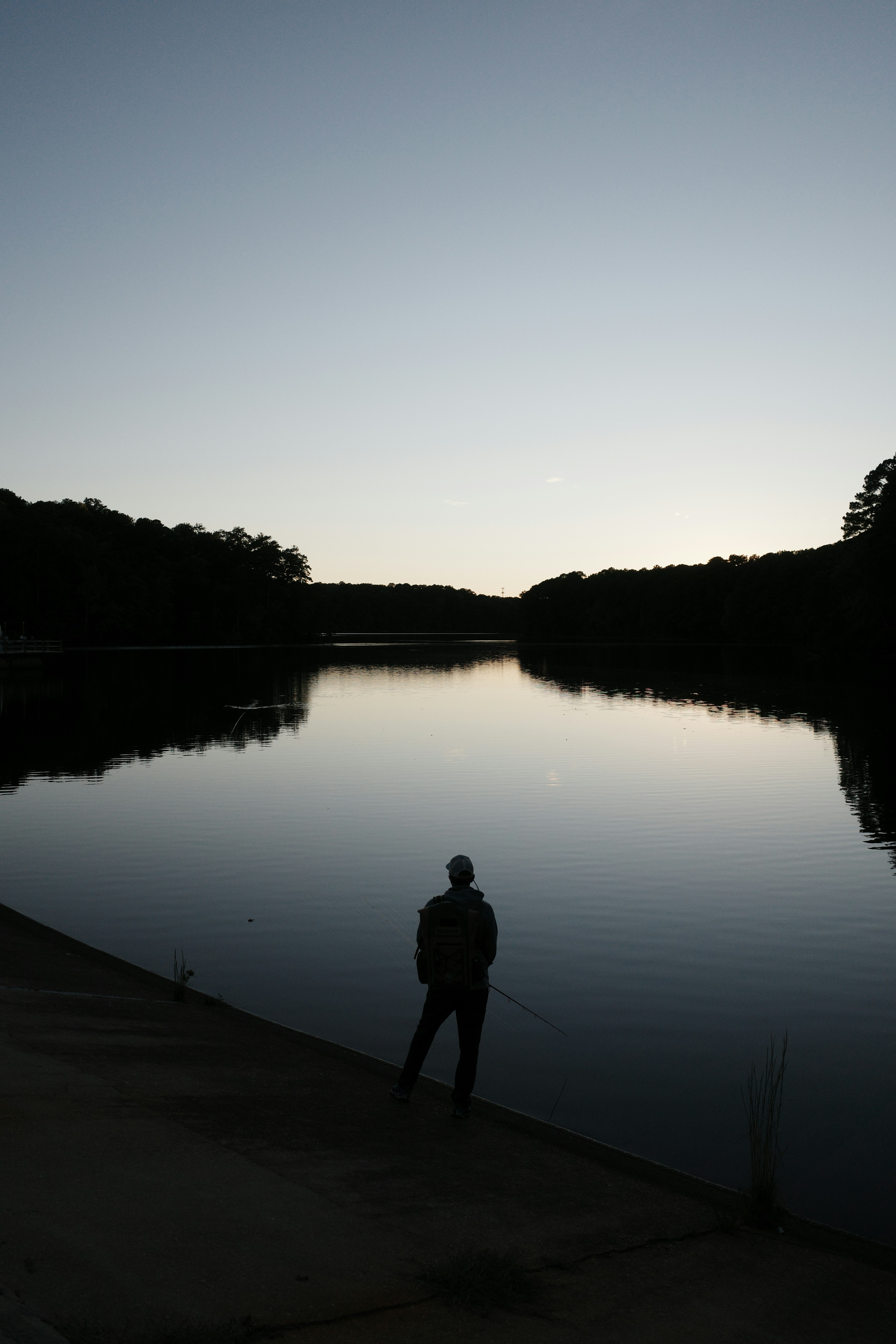 Silhouette by the Lake: A Lone Angler at Dusk