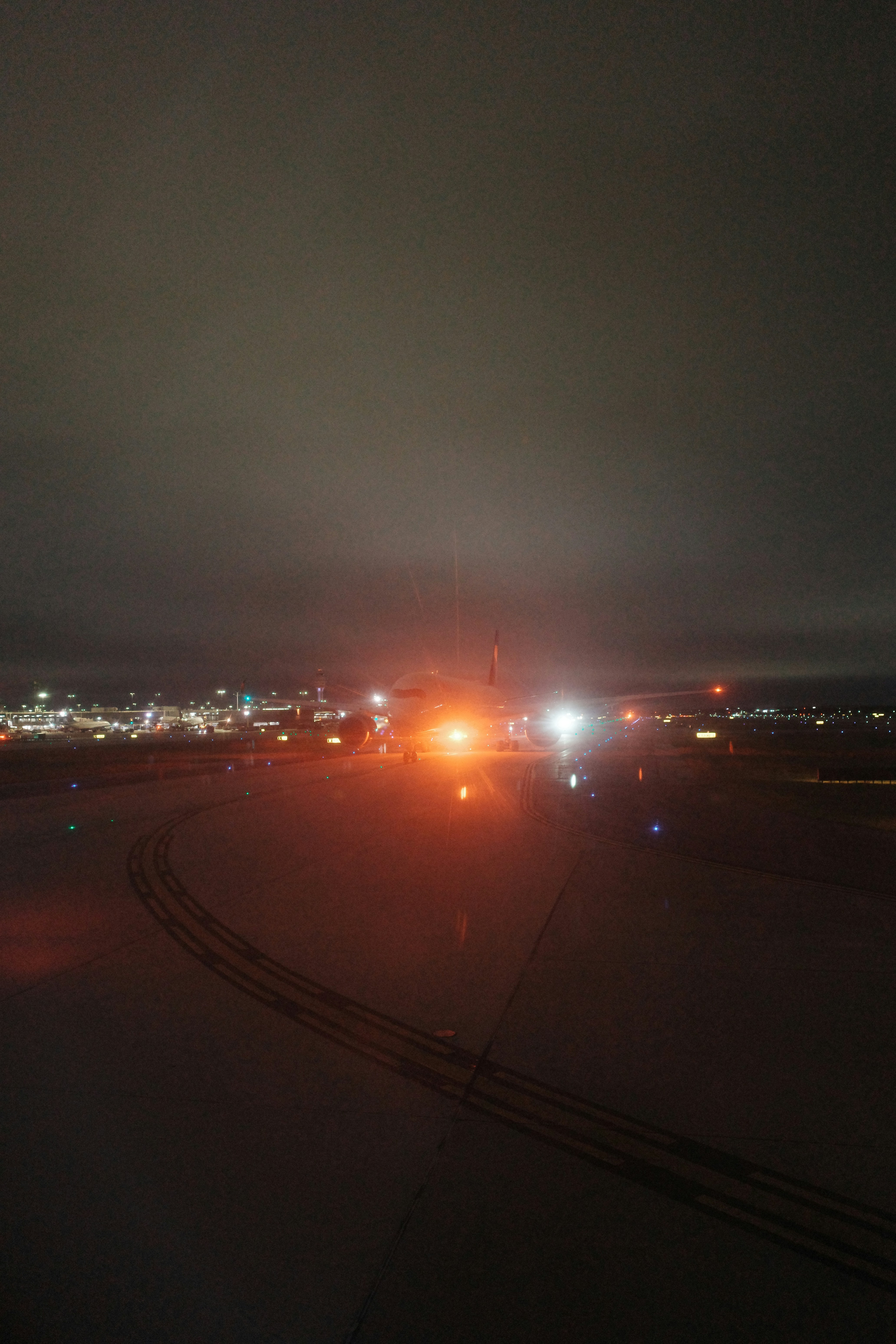 An airplane taxiing on a dark runway at night with bright landing lights