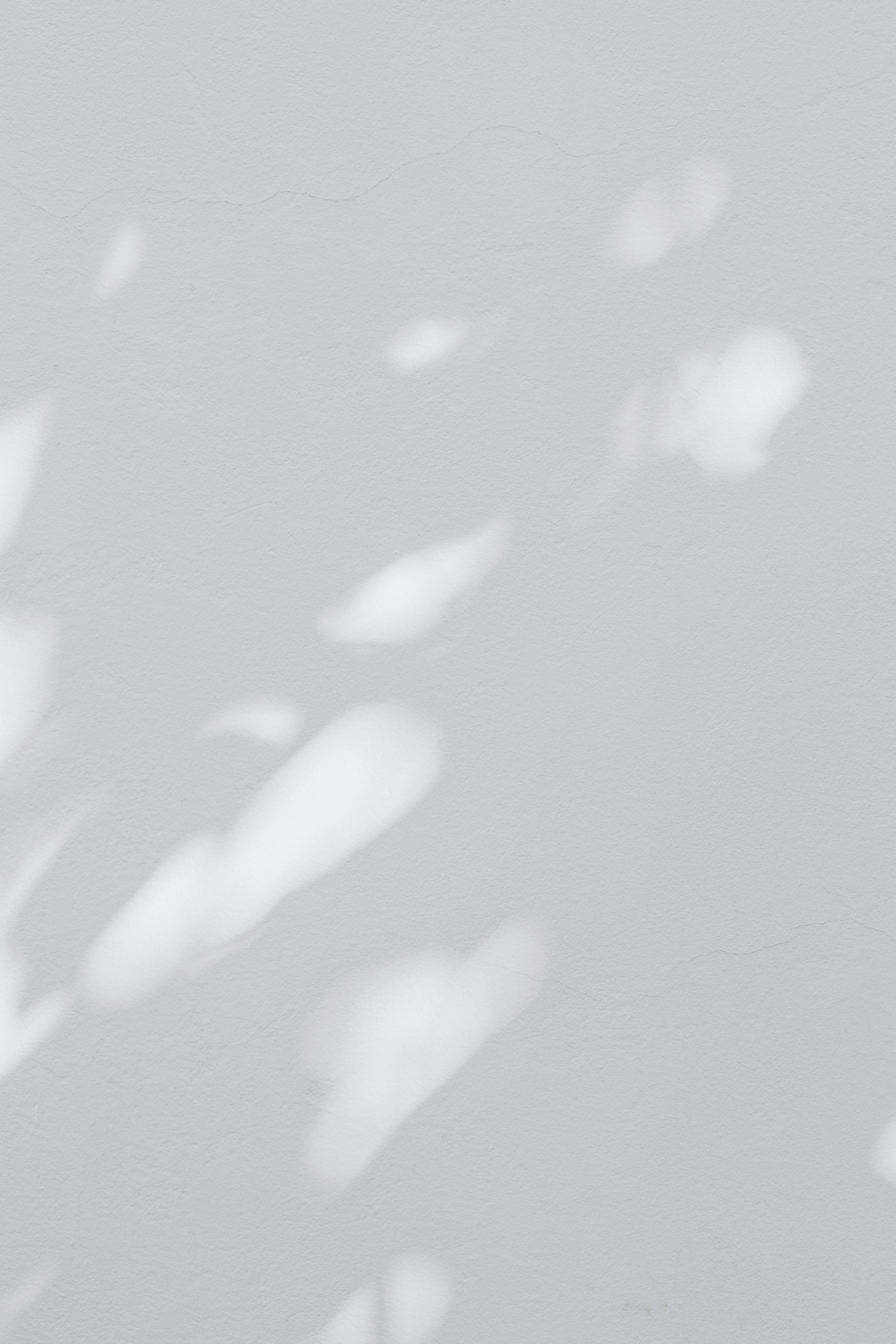 Soft, out-of-focus white shapes drift across a pale wall, creating an abstract play of light and texture. This piece emphasizes mood and negative space without a defined subject or scene.